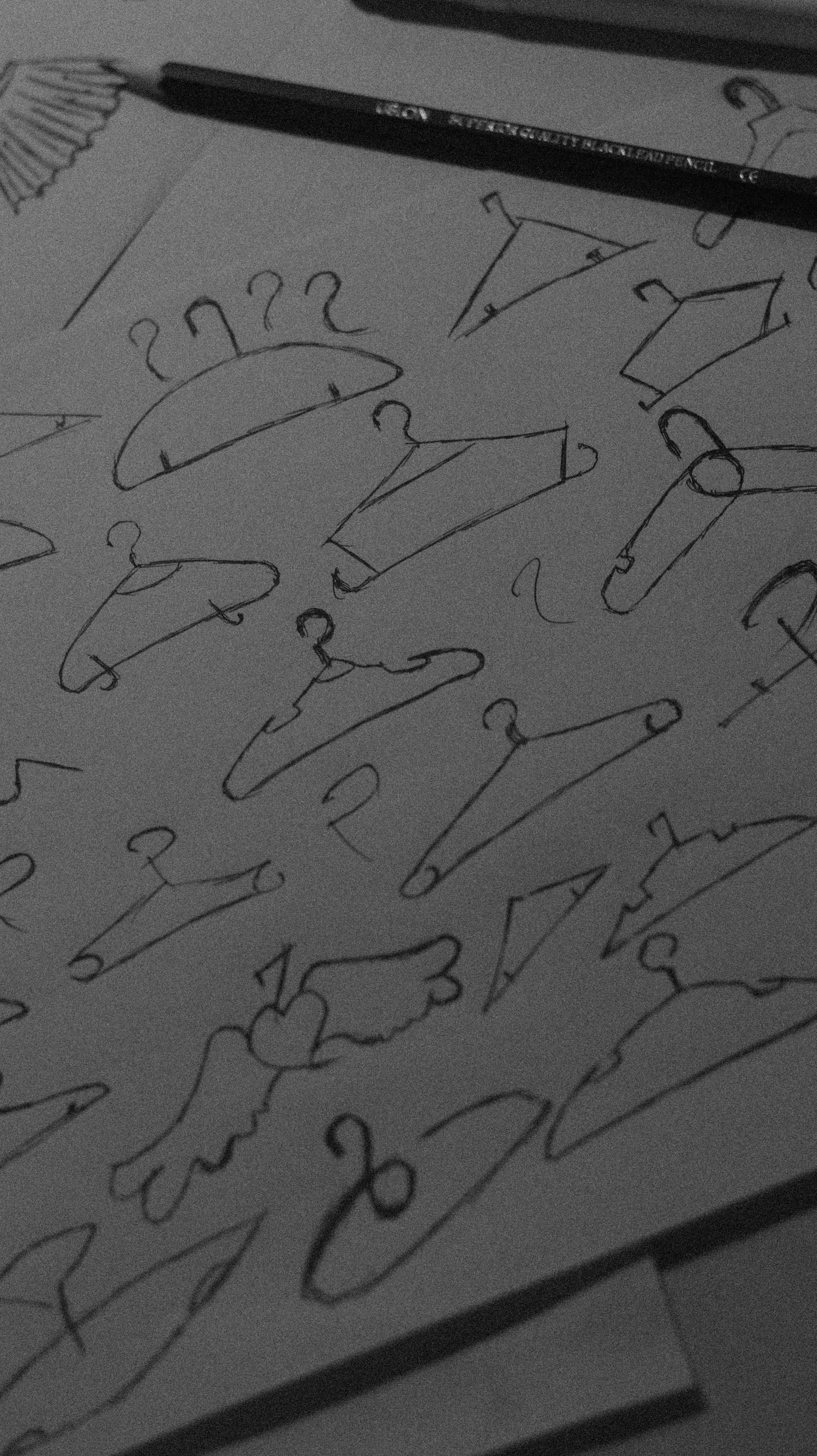 Sketches of coat hangers on paper with pencils.