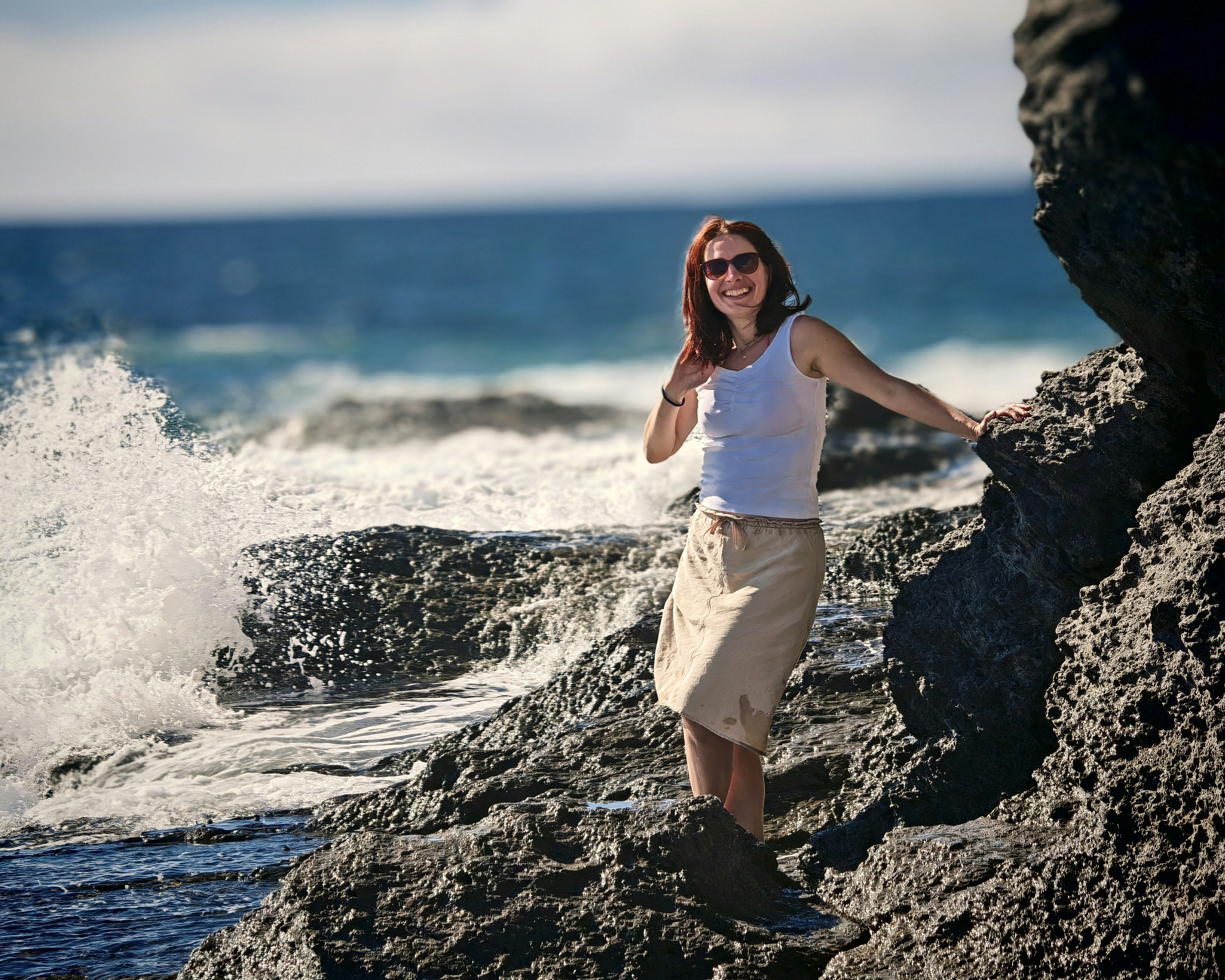 Woman smiling on rocky beach with ocean waves