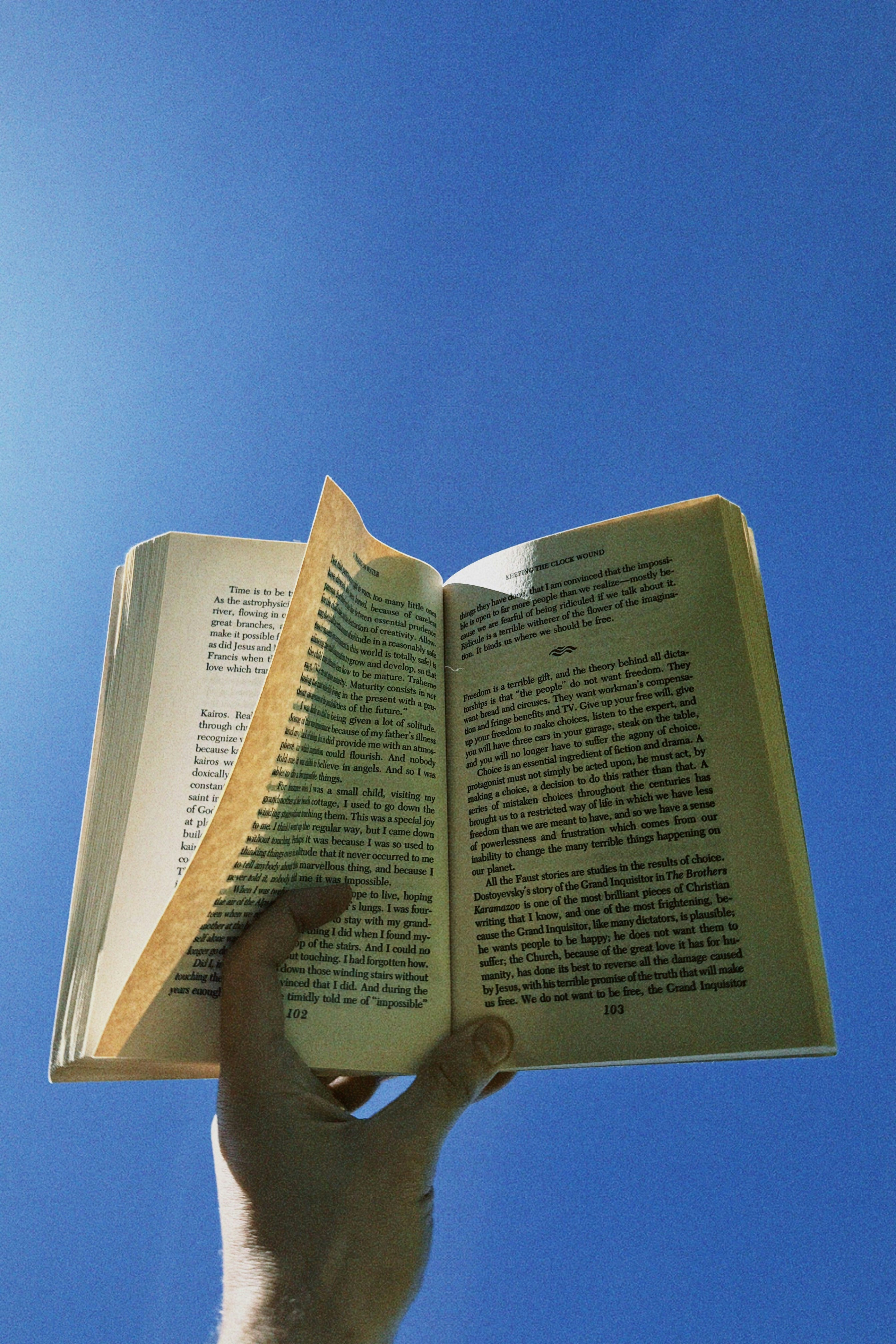 Reading a book outside | Hand holding open book against blue sky