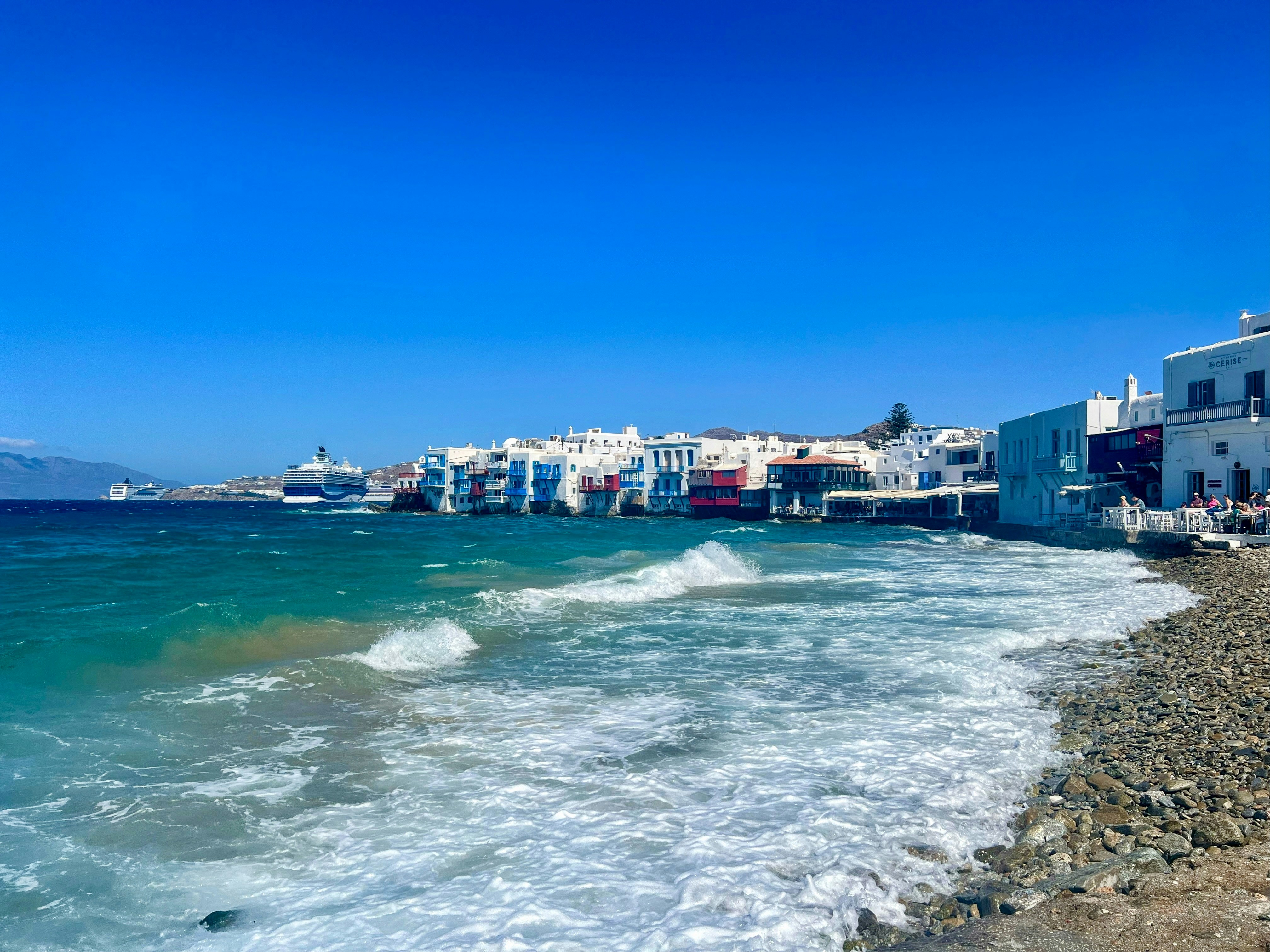 Little Venice in Mykonos | White buildings line a turquoise ocean with crashing waves.