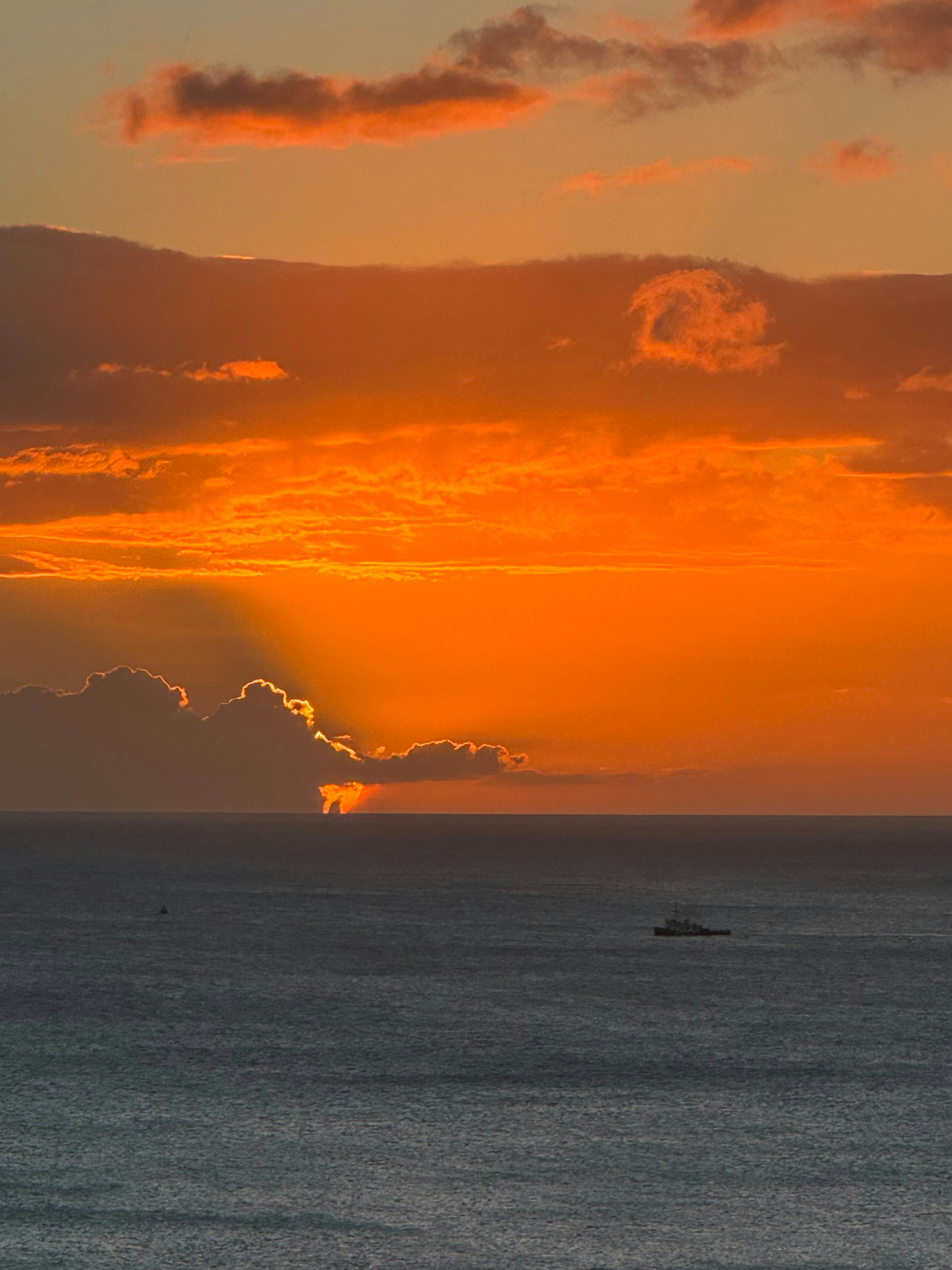 Vibrant sunset casting golden hues over the ocean, with a silhouette of a distant boat on the serene water. 