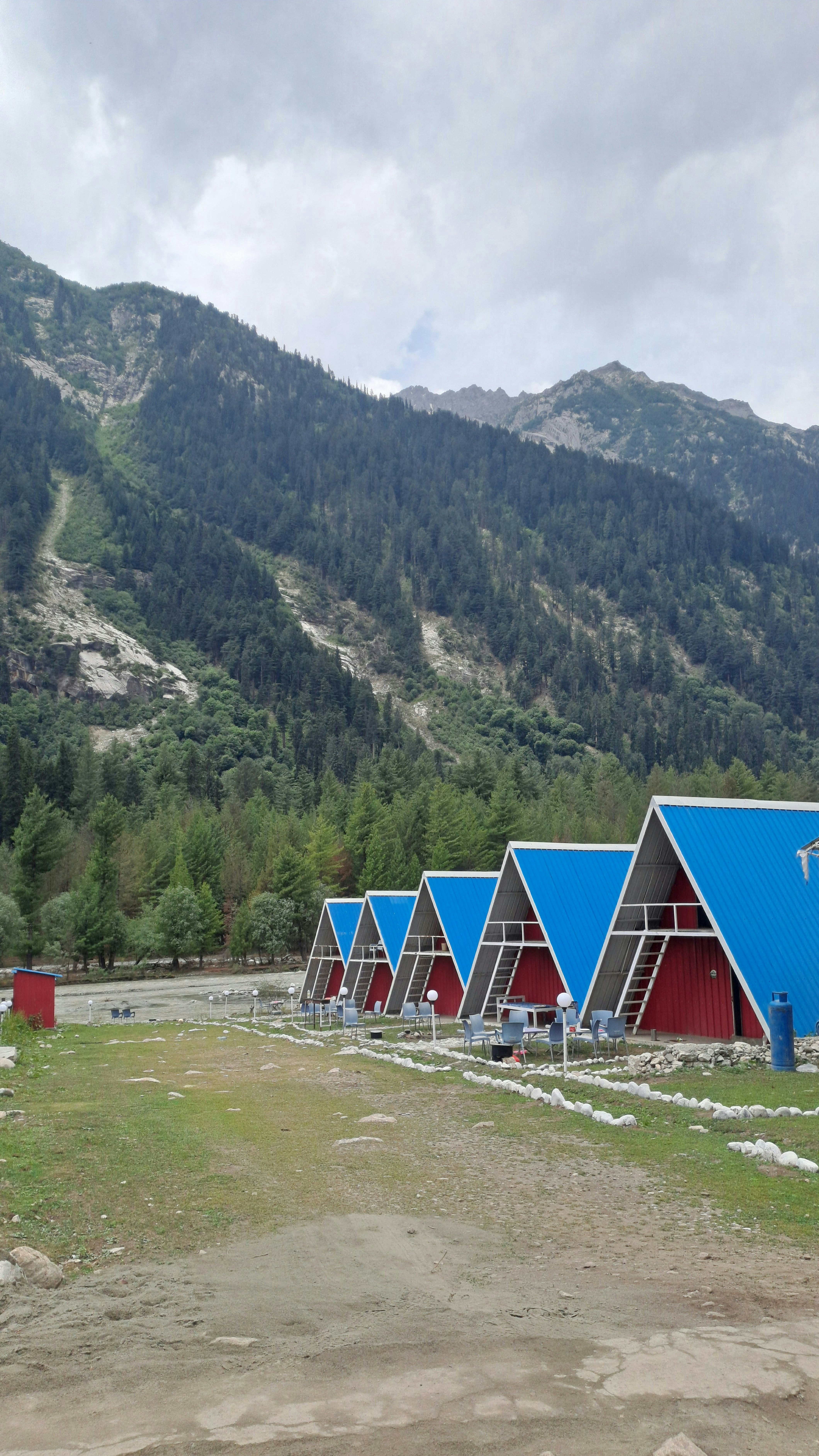 Colorful A-frame cabins nestled in a lush valley, surrounded by towering mountains and a serene landscape. Ideal for a peaceful getaway.
