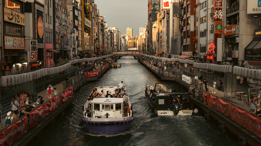 Two tour boats moving down a crowded city canal flanked by lanterns and riverside eateries at dusk.