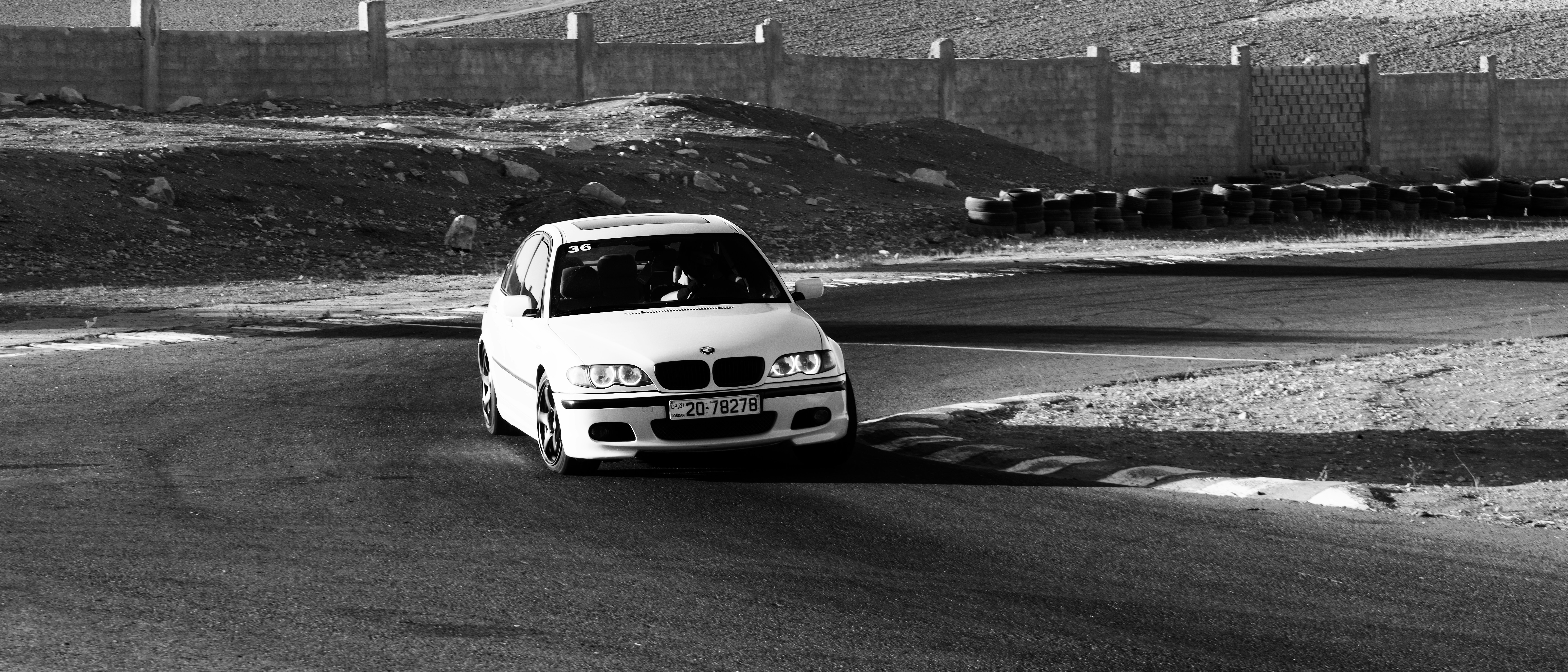 A white BMW skillfully navigating a curve on a racetrack, showcasing dynamic motion and precision handling.