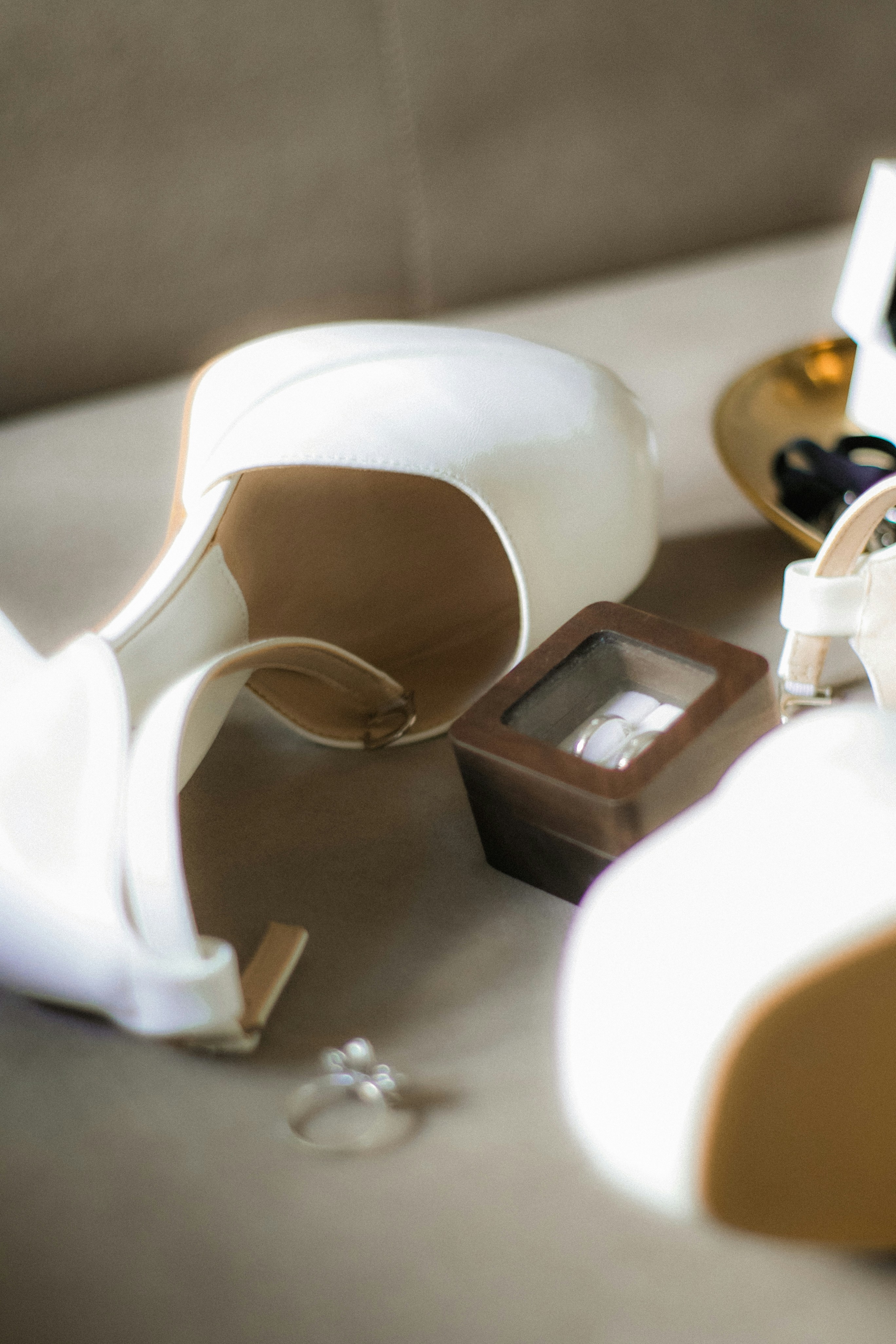 White high-heeled shoes paired with a wooden ring box and sparkling jewelry, arranged on a soft surface. A glimpse into bridal preparations.