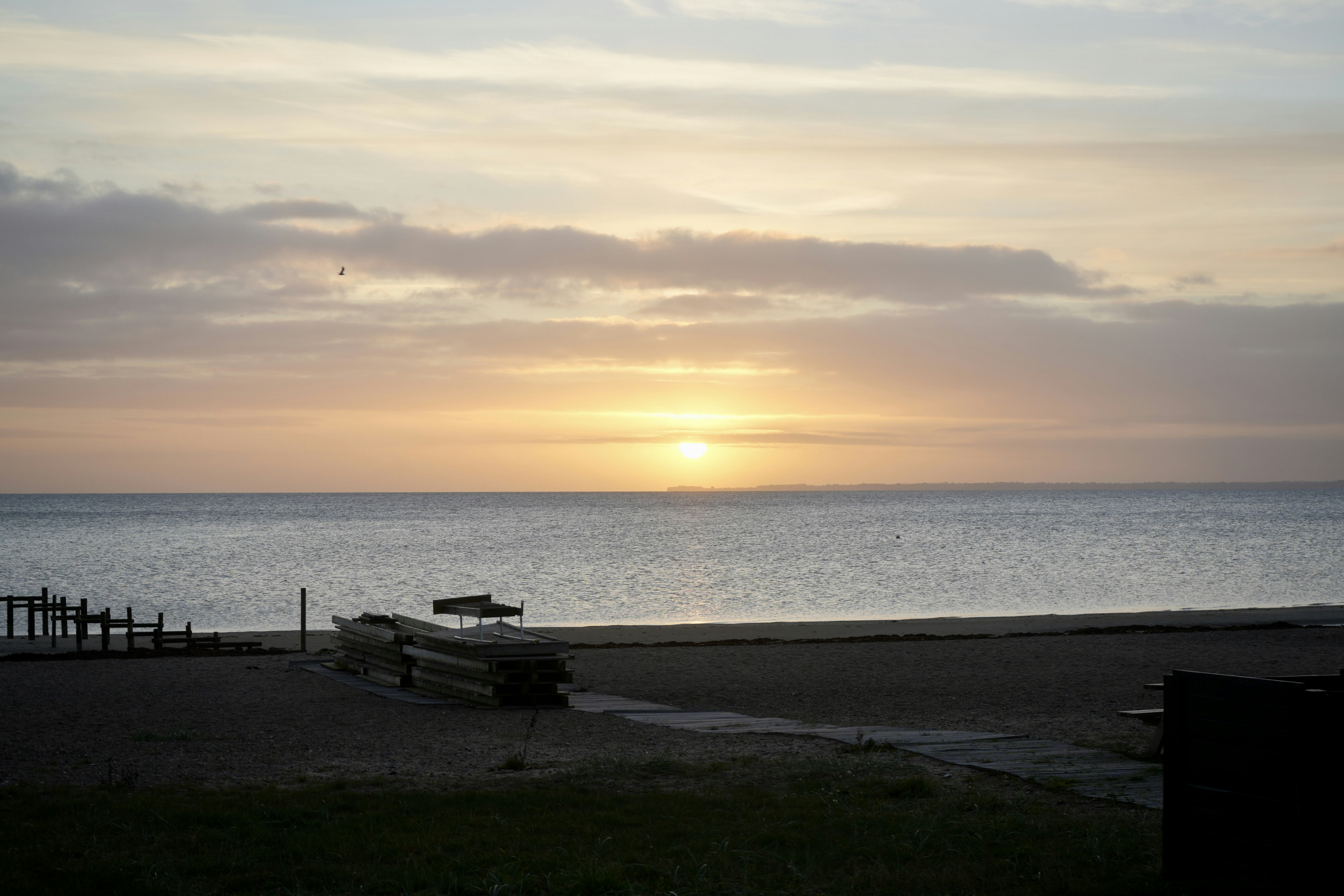 Sunset over a calm ocean with a beach.