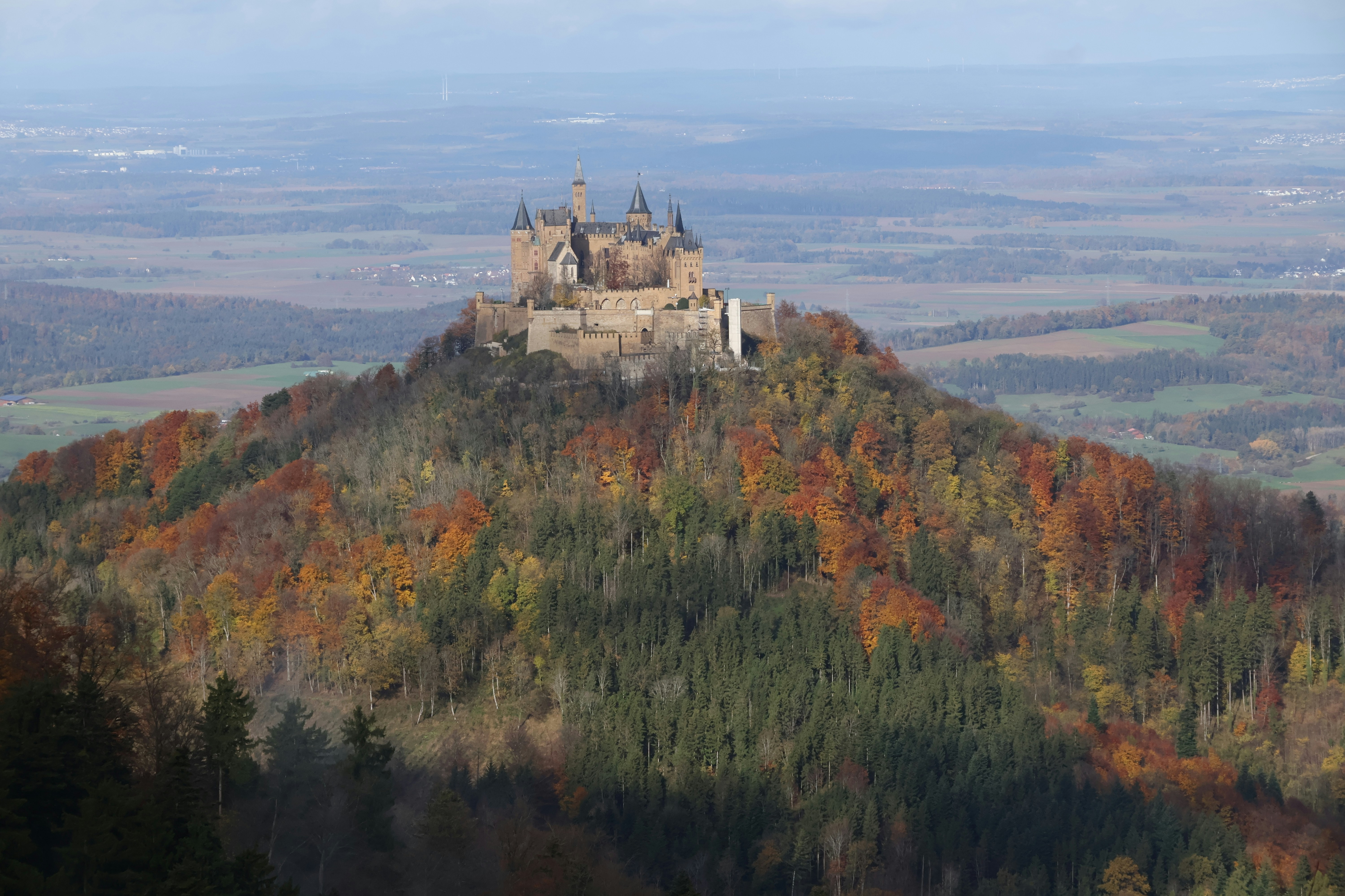 A majestic castle perched atop a hill, surrounded by a vibrant tapestry of autumn foliage. The expansive landscape stretches into the distance.