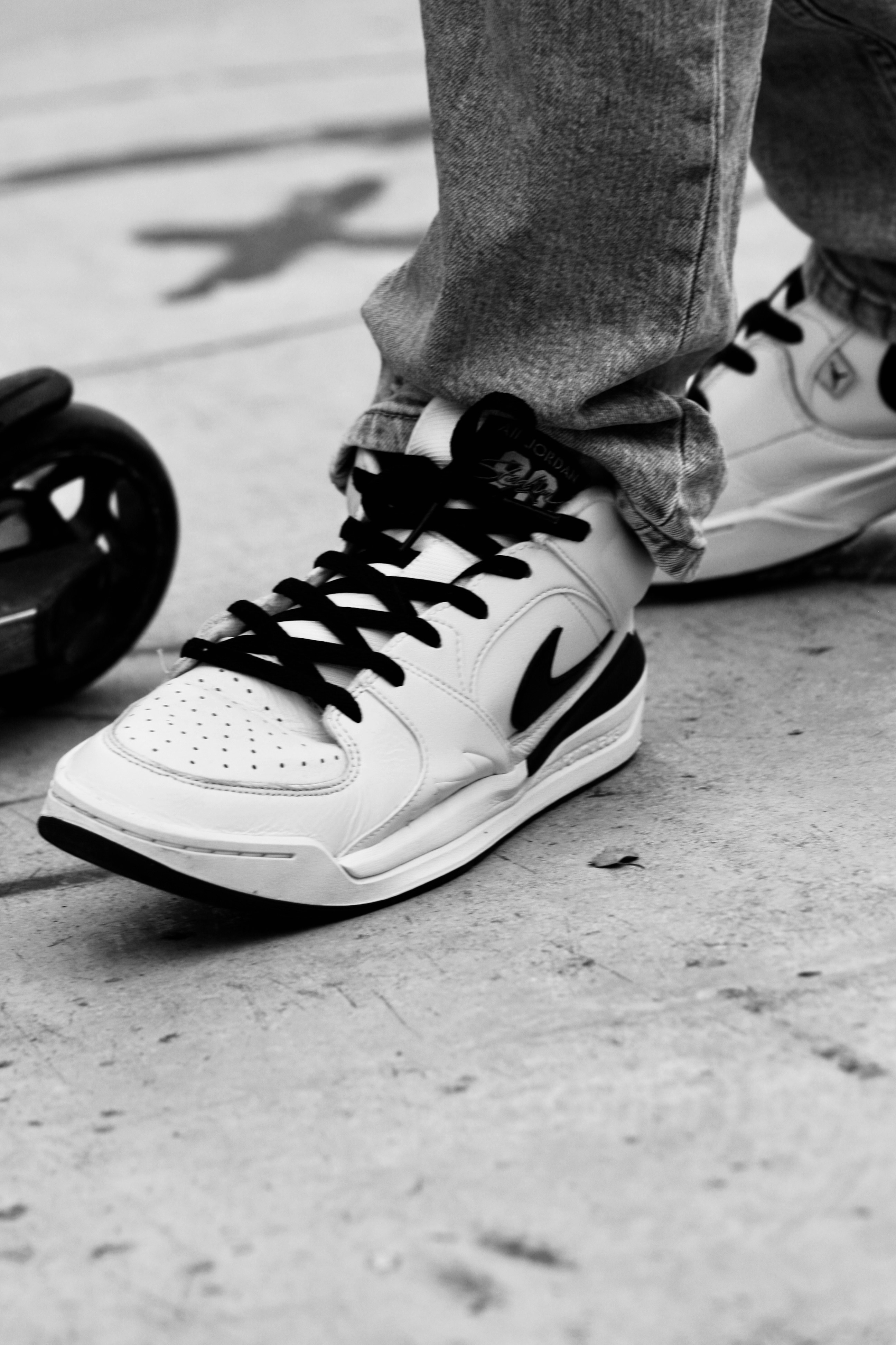 Close-up of a stylish sneaker paired with denim, set against an urban backdrop. The black and white contrast emphasizes the shoe's design.