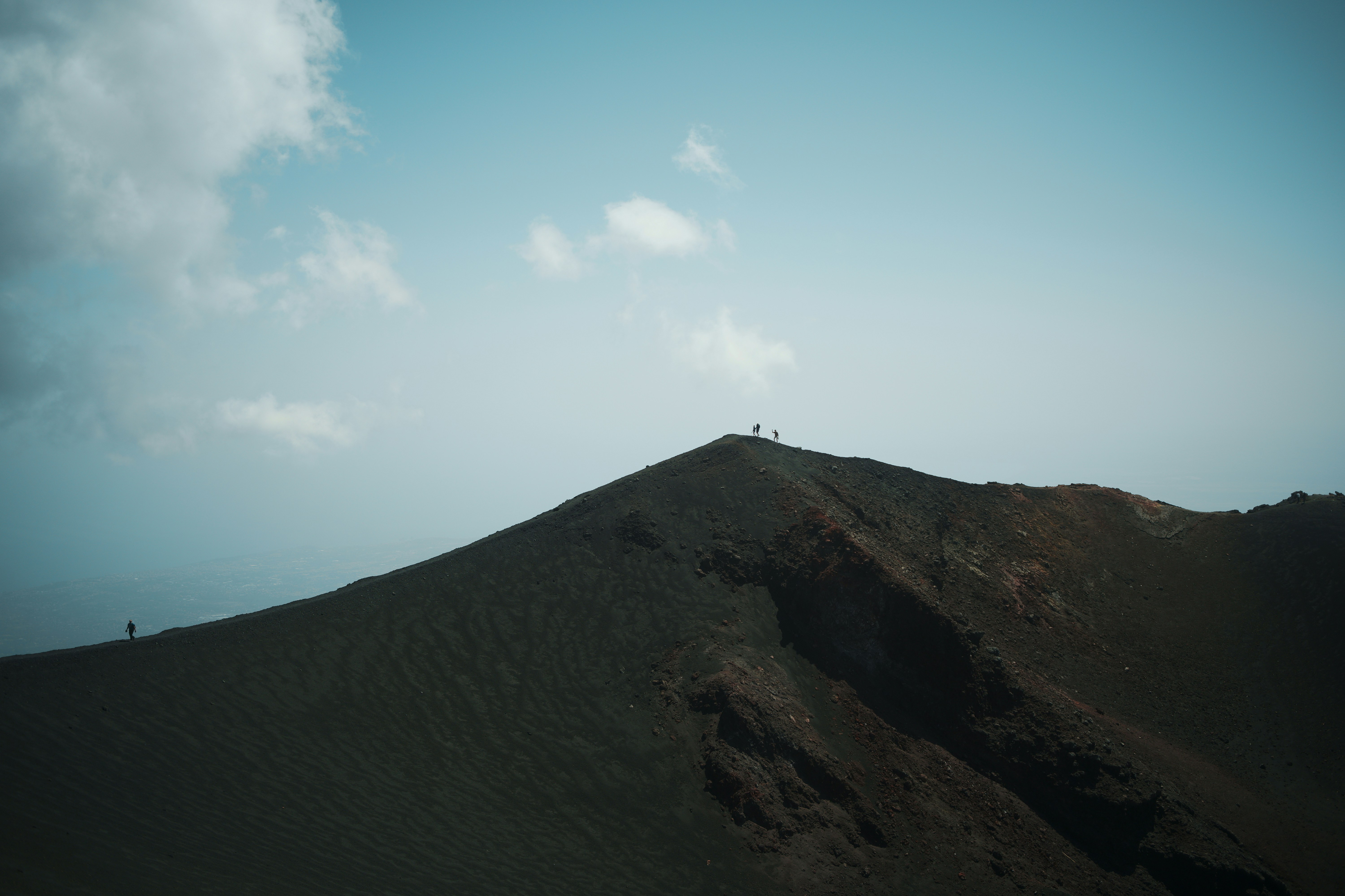 People on a dark volcanic mountain ridge under sky