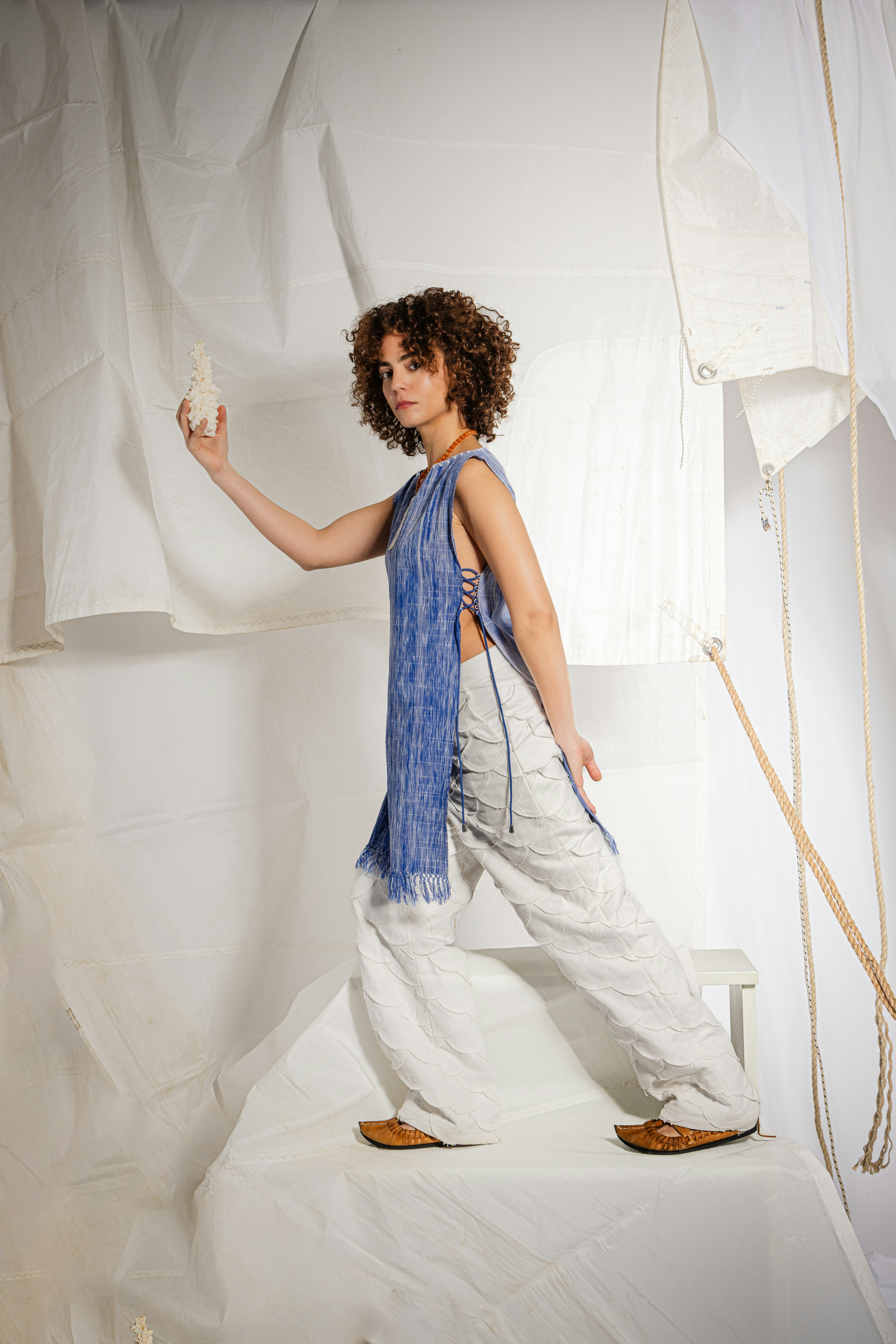 Woman in blue tunic and white pants holds object