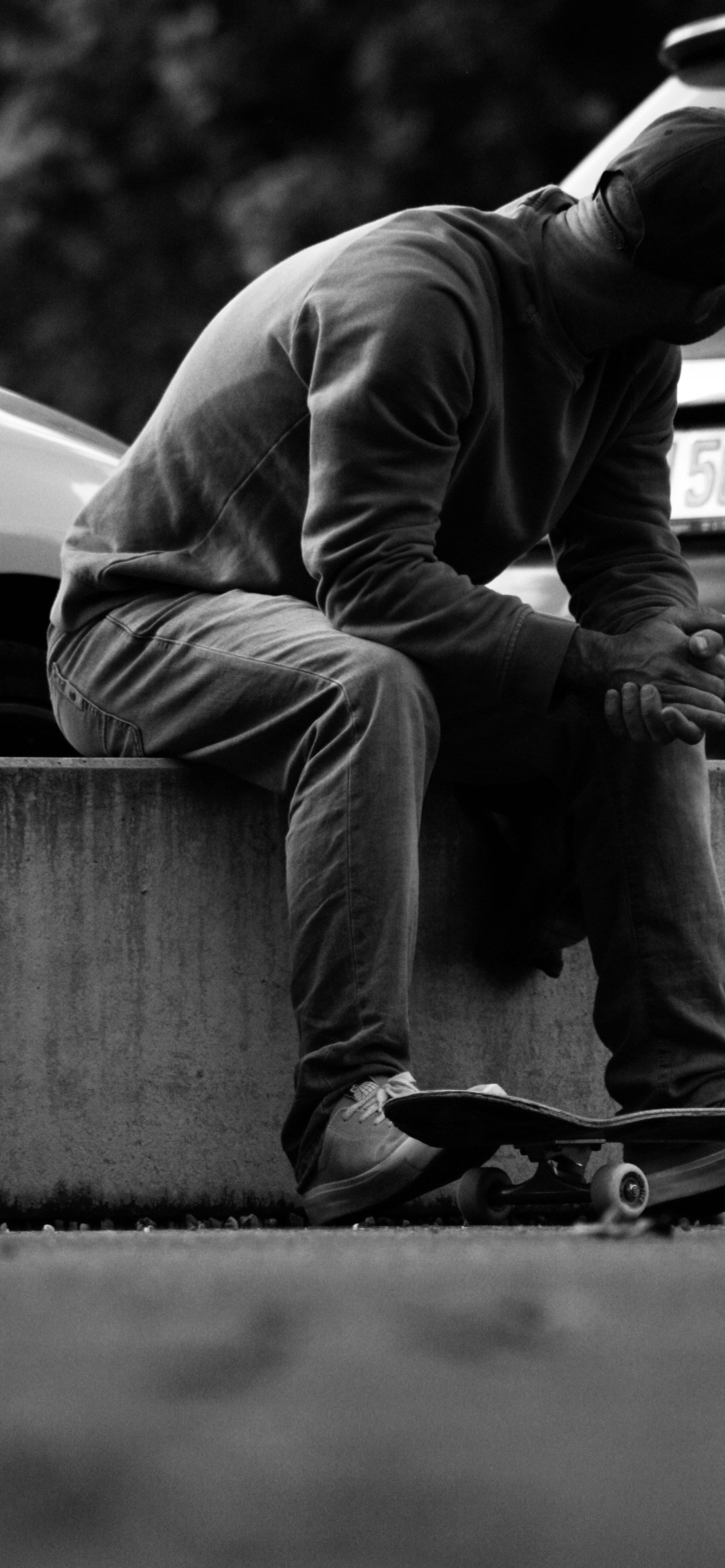 Man sitting with skateboard next to concrete ledge