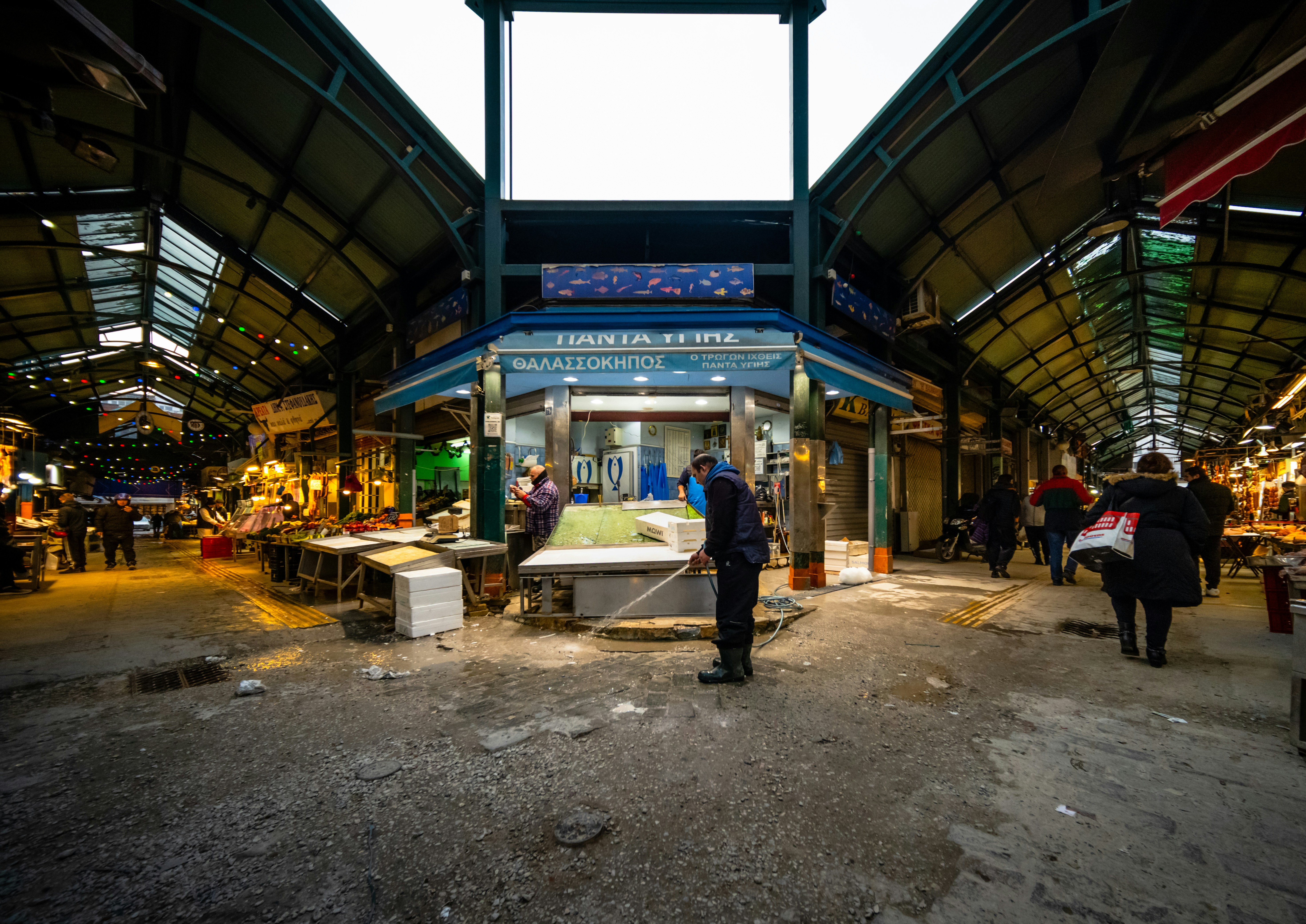 Vibrant marketplace bustling with activity, featuring vendors and shoppers amidst colorful stalls. The central kiosk serves as a focal point for trade and interaction.