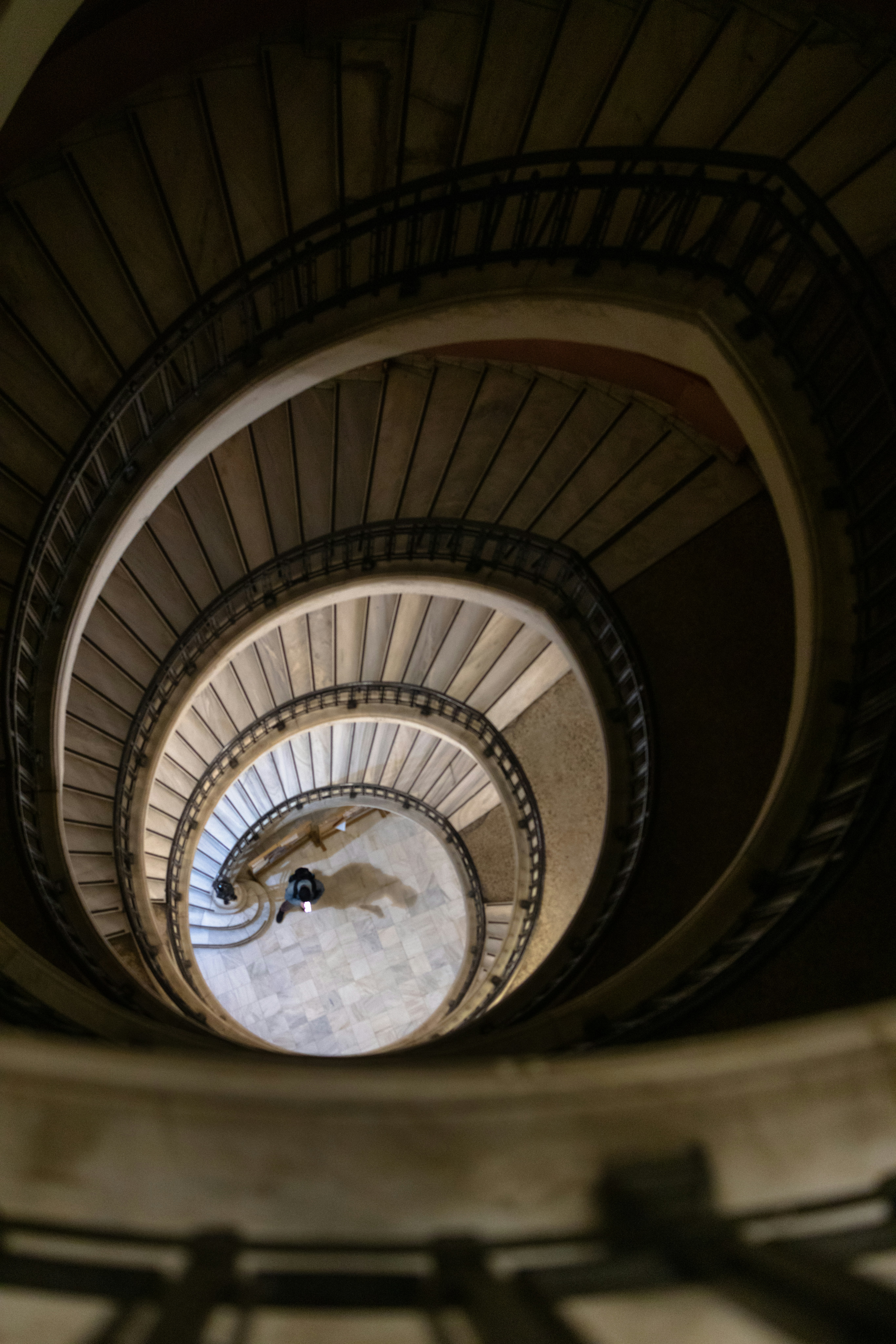 Aerial view of a spiraling staircase with a lone figure ascending, highlighting the intricate architectural design and symmetry.