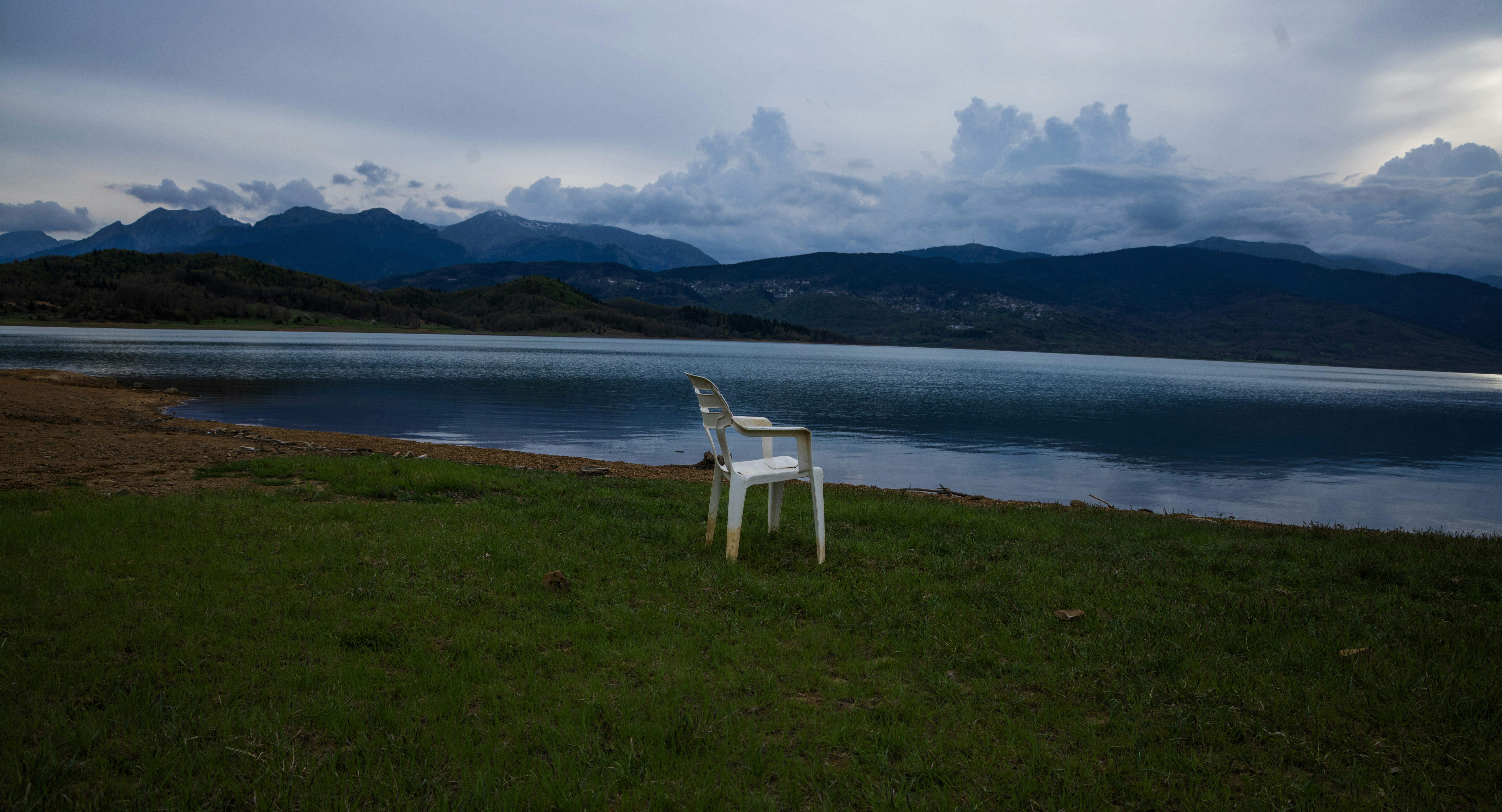 White chair on grassy shore overlooking lake and mountains.