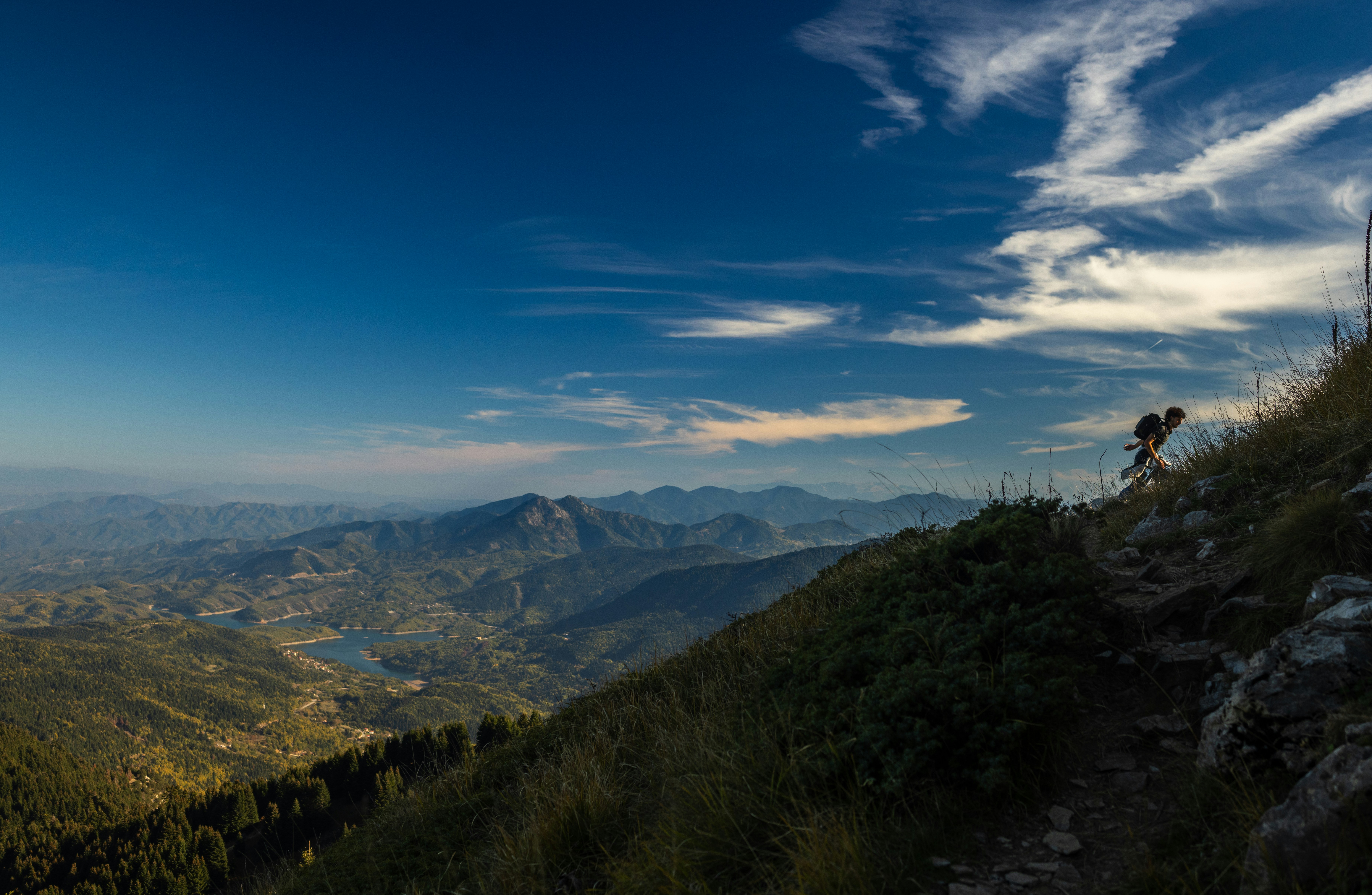 A hiker walks on a mountain trail overlooking a valley.