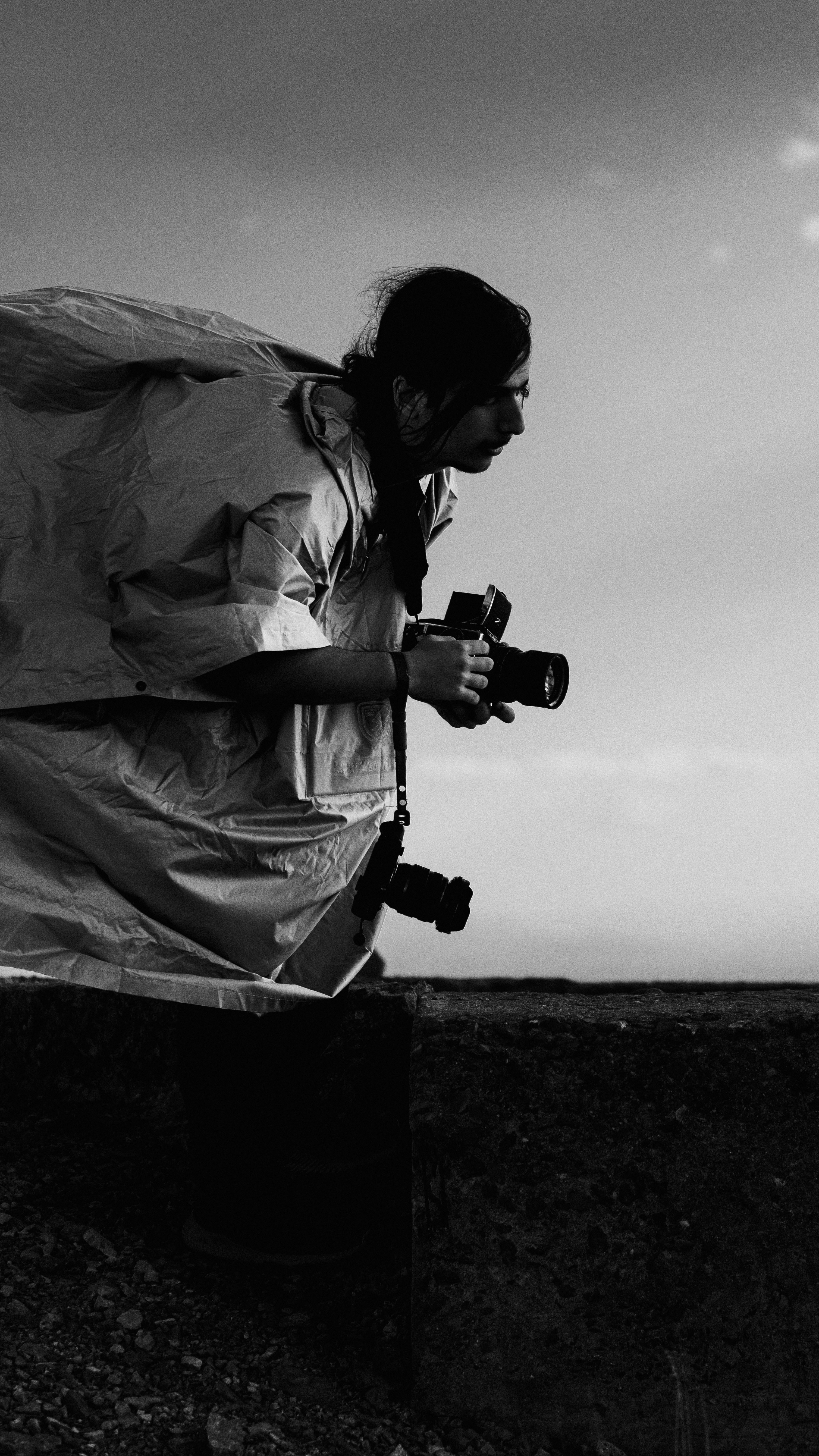 Person in poncho holds camera against sky.