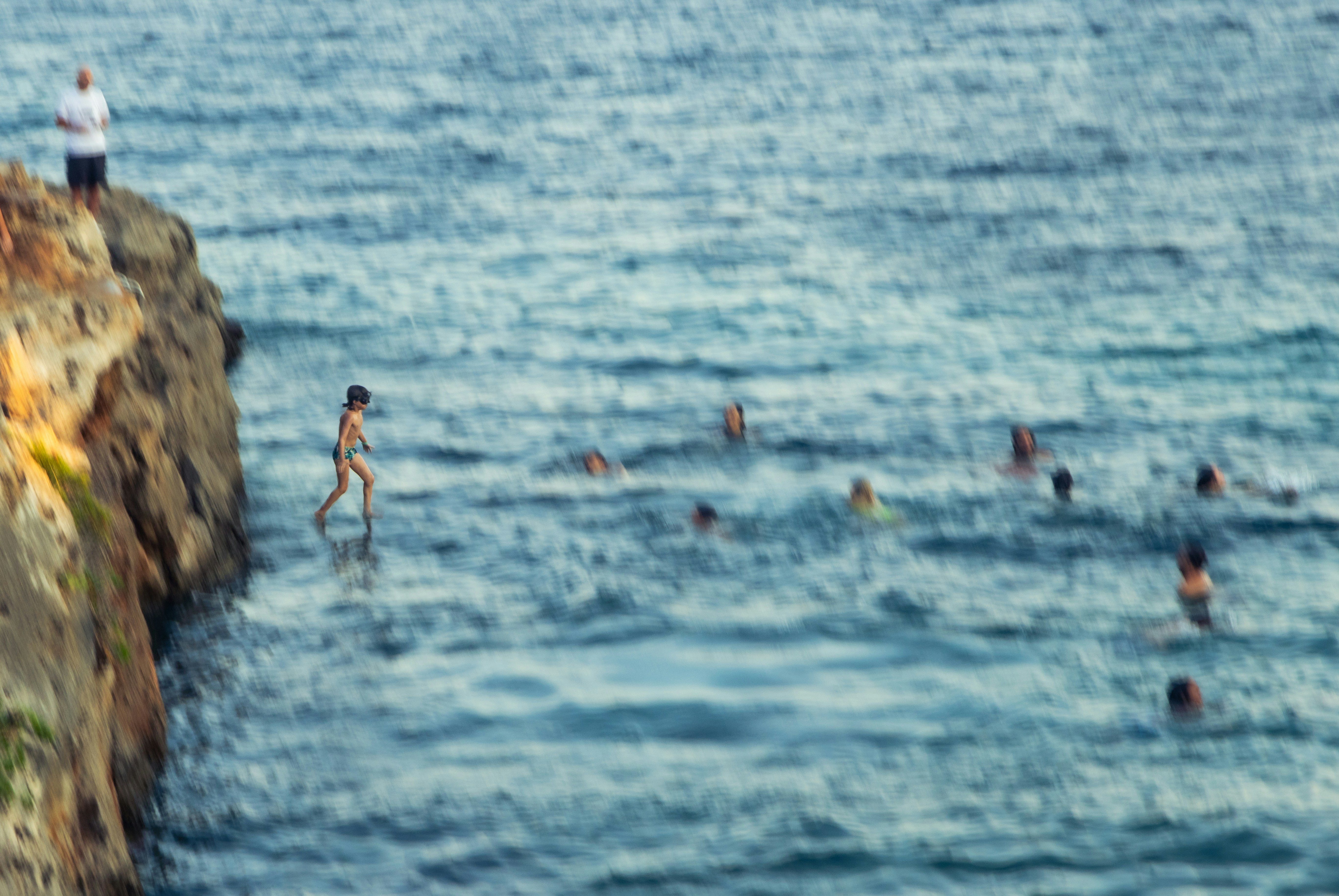 People swim and one person stands on cliff edge. photo – Free Sea Image ...