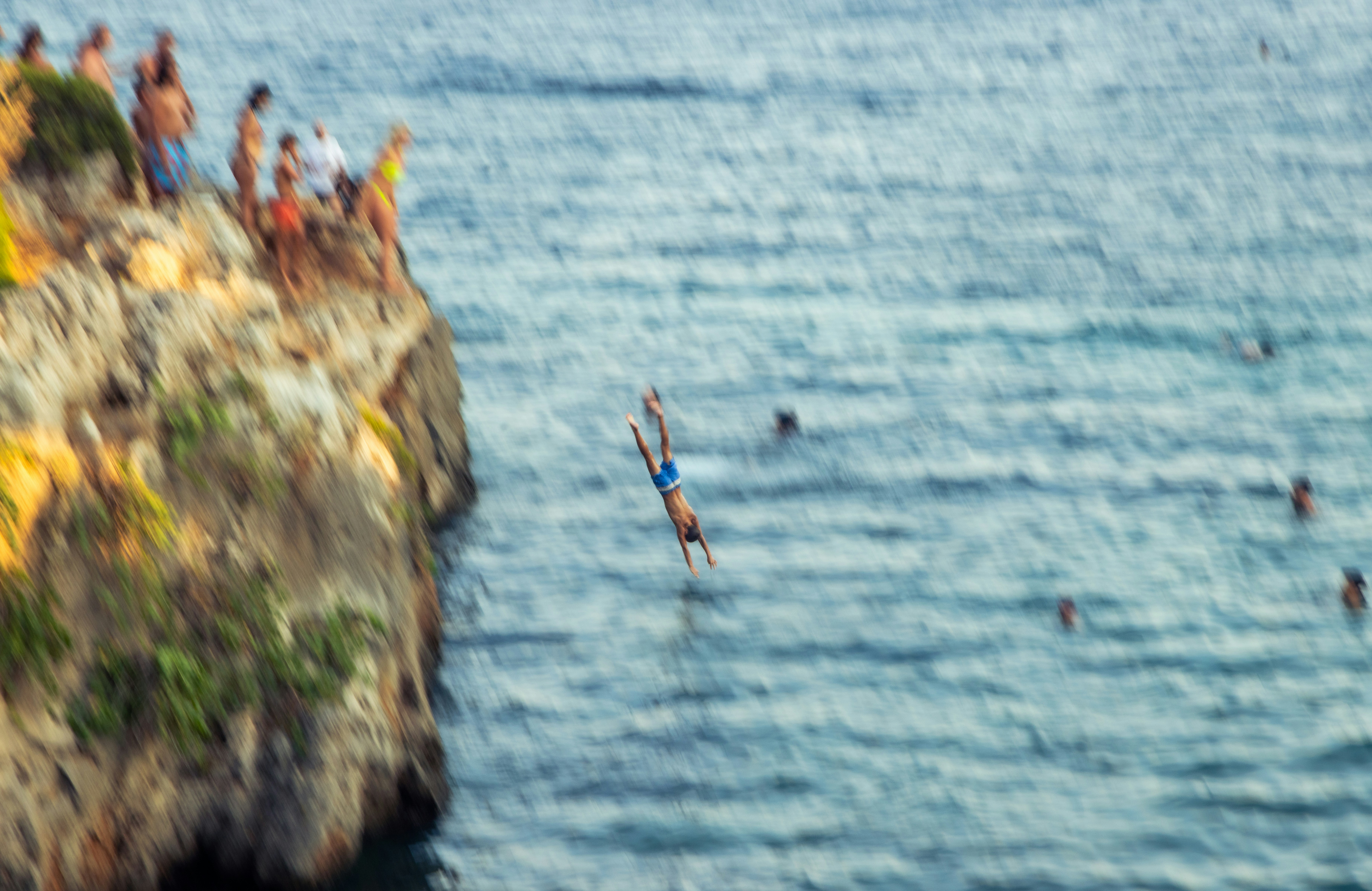 Man jumps off a cliff into the ocean.