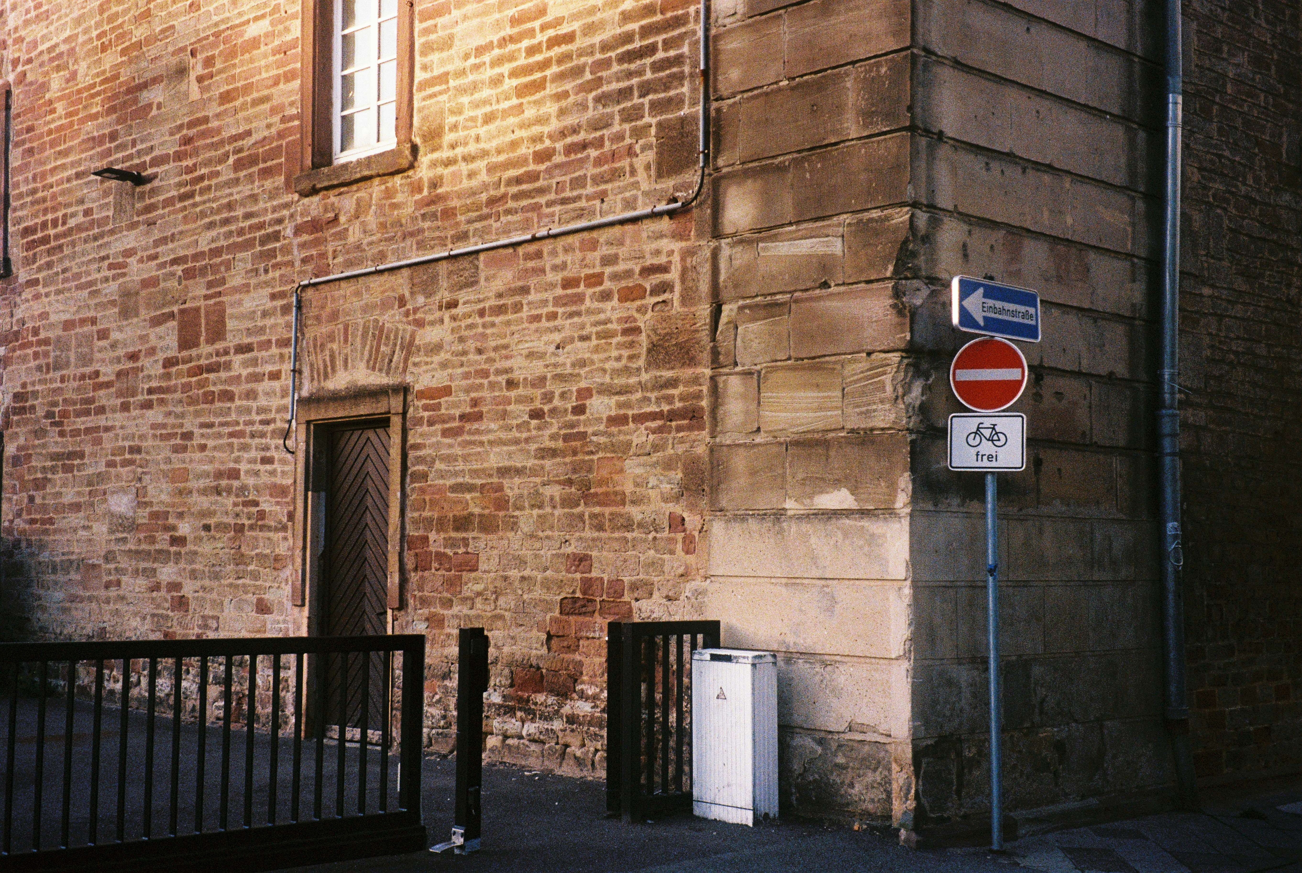 Shot on Kodak UltraMax 400 | Brick building corner with street signs and trash cans.