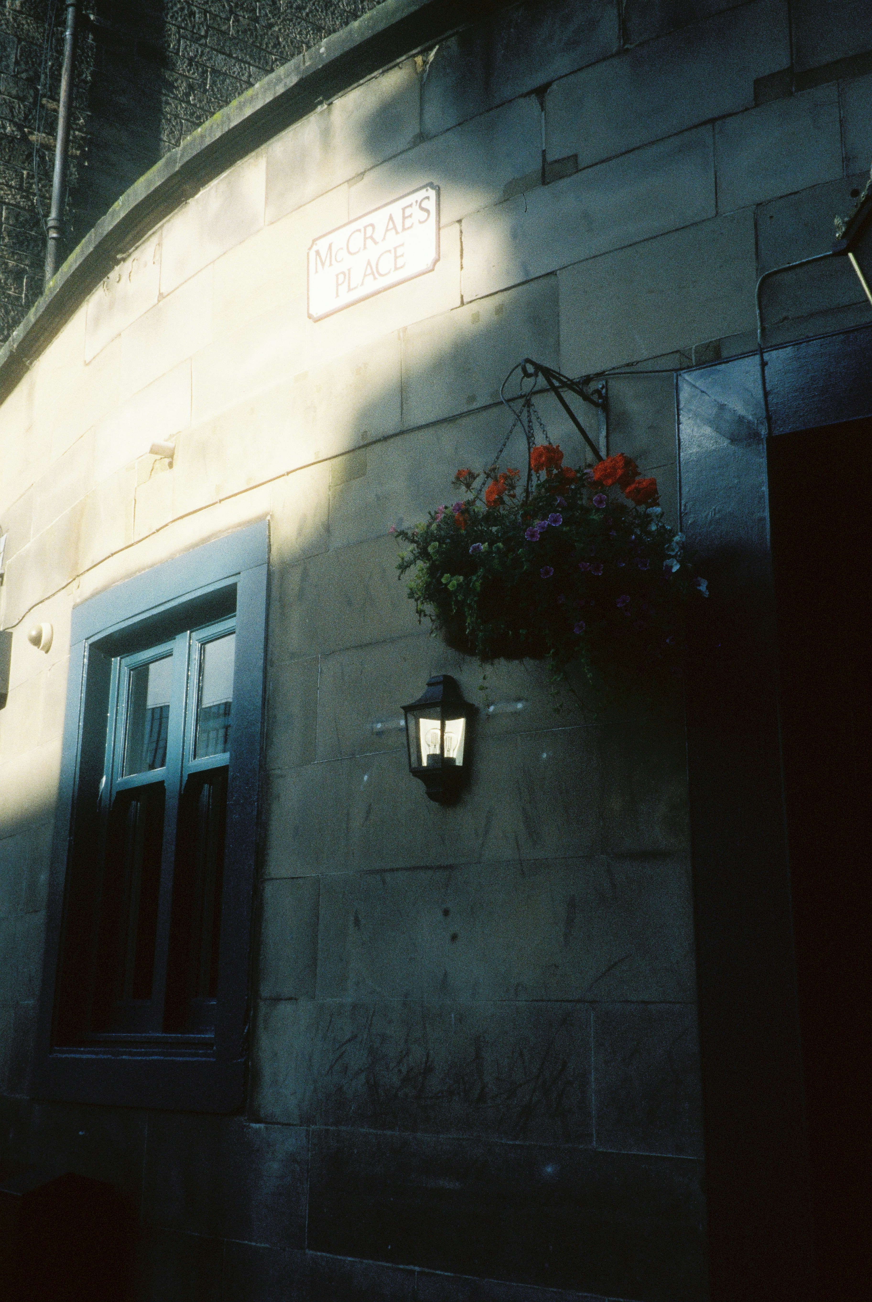 Shot on CineStill 800T | Stone building with window, lamp, and hanging flowers.
