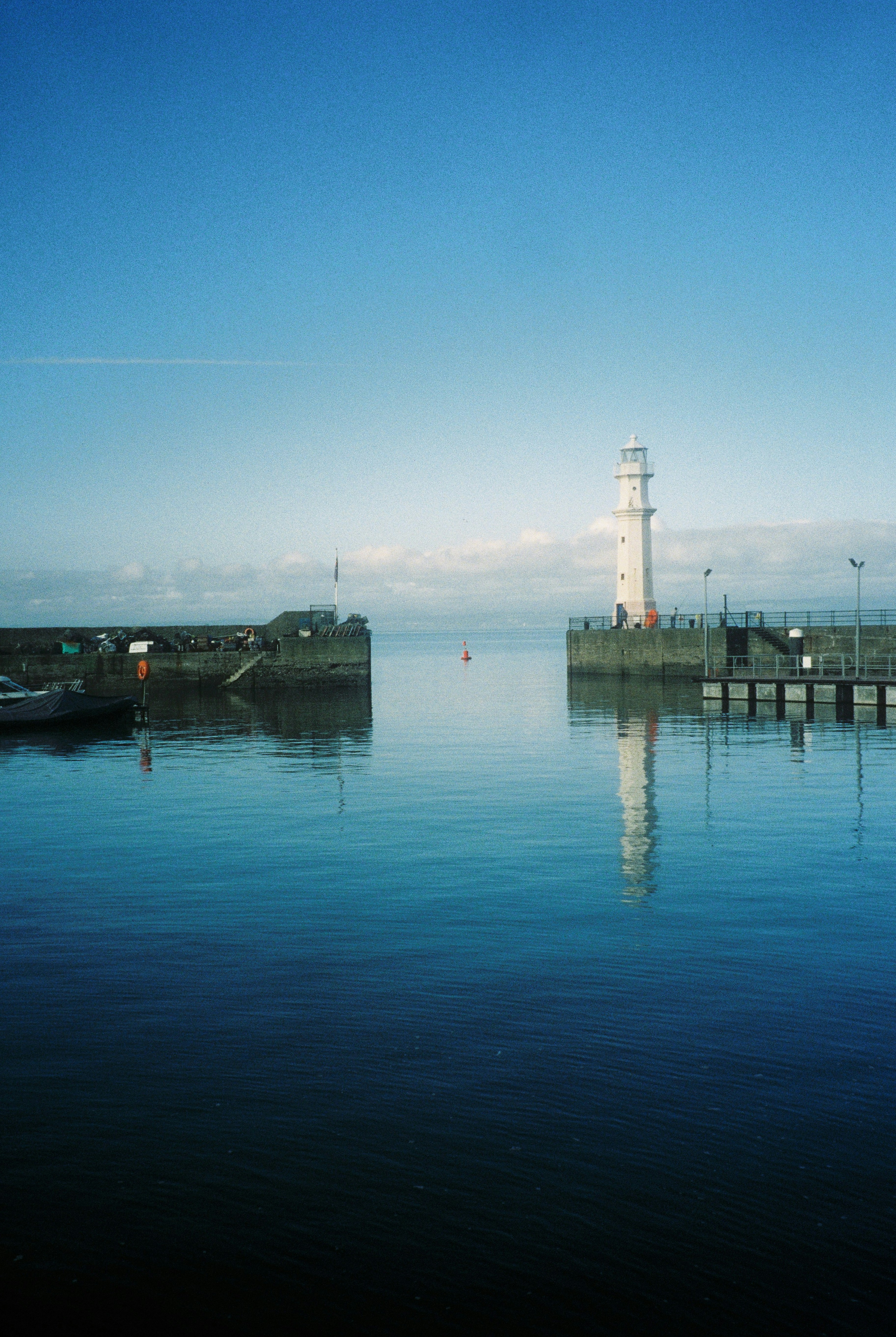 Shot on CineStill 800T | White lighthouse on a pier overlooking calm blue water