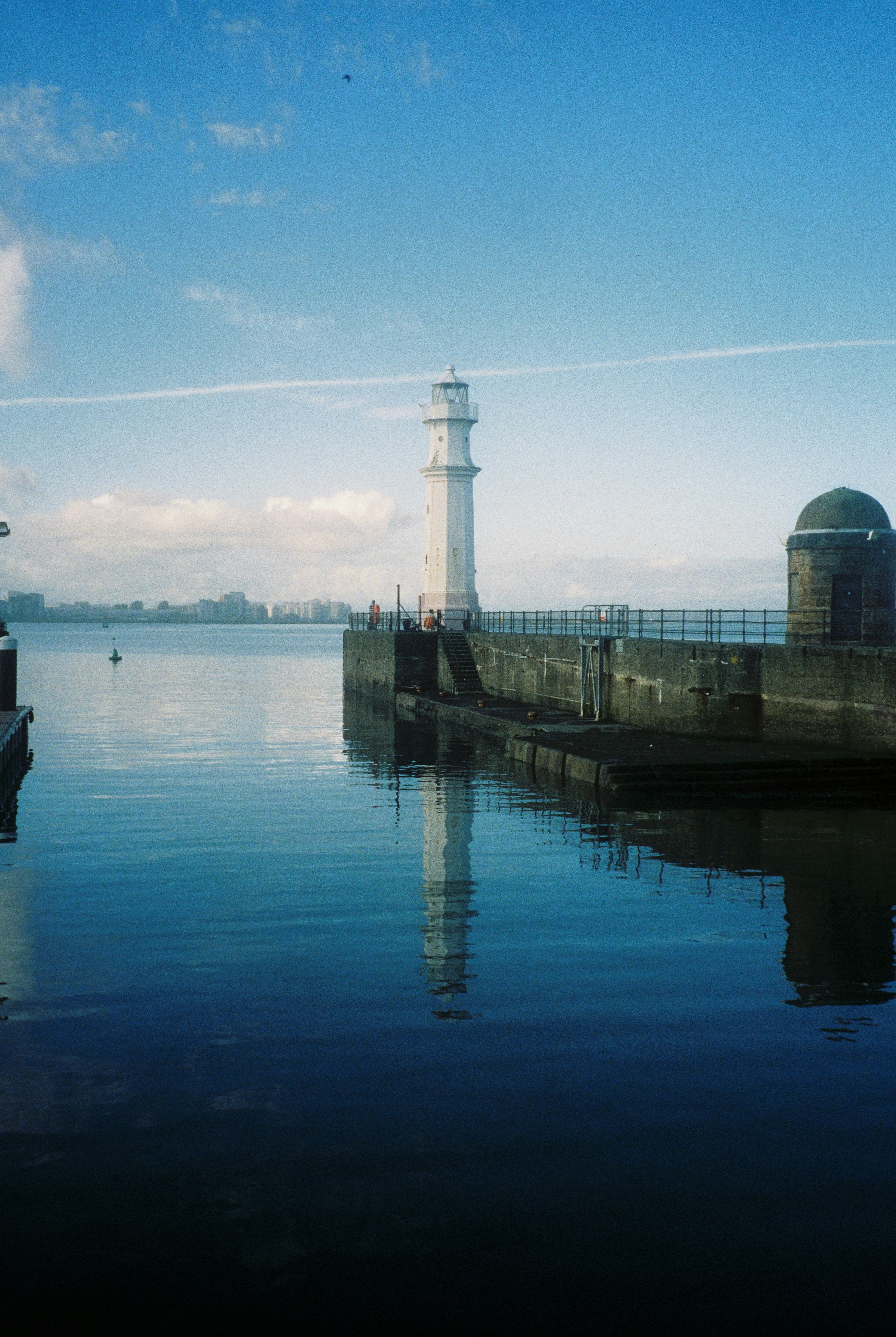 Shot on CineStill 800T | White lighthouse on a pier with calm blue water