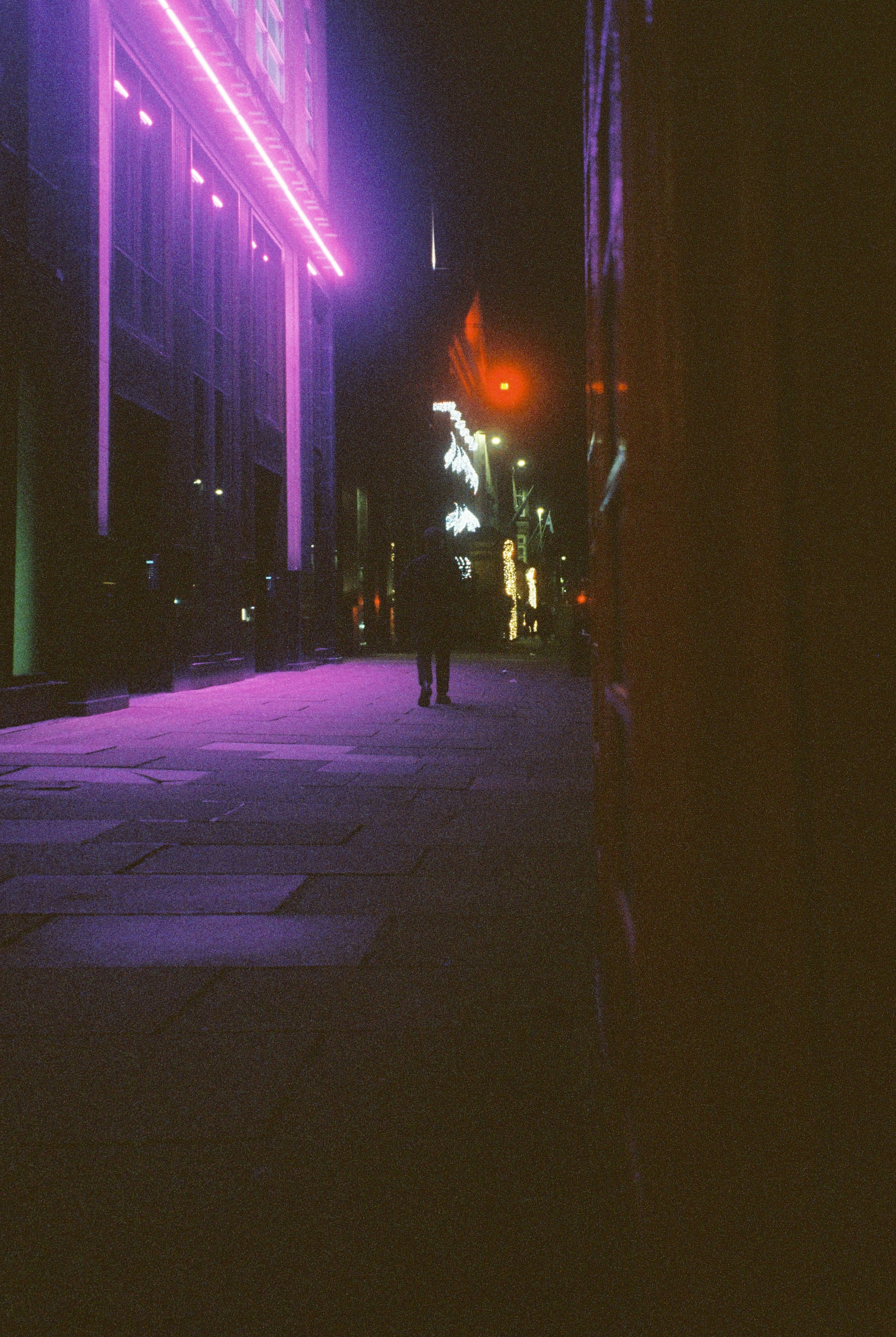 A solitary figure walks along a dimly lit street adorned with vibrant neon lights, creating a surreal atmosphere at night.