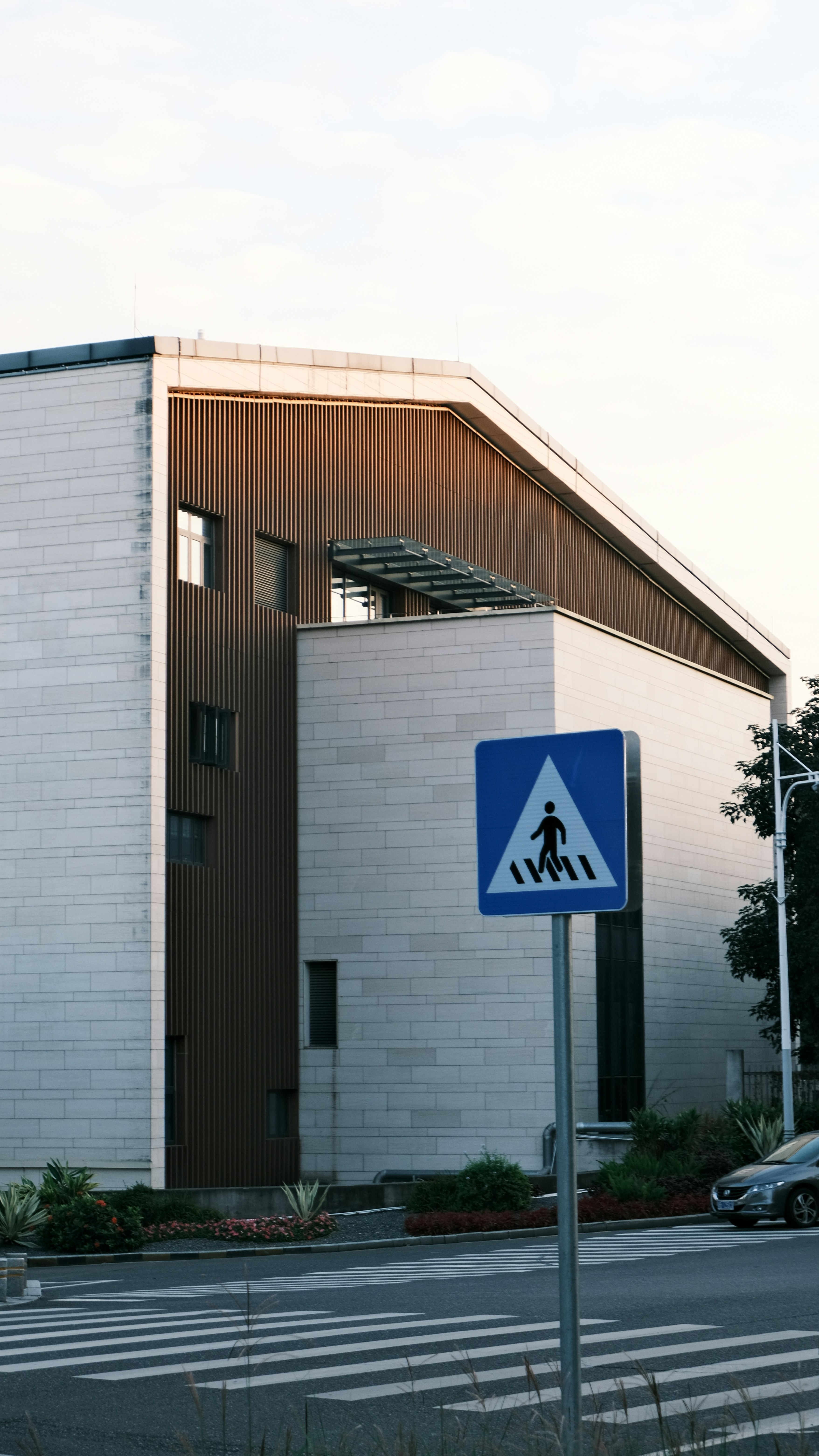 Modern building with a striking facade complemented by a pedestrian crossing sign in the foreground. The interplay of materials and colors enhances the urban landscape.