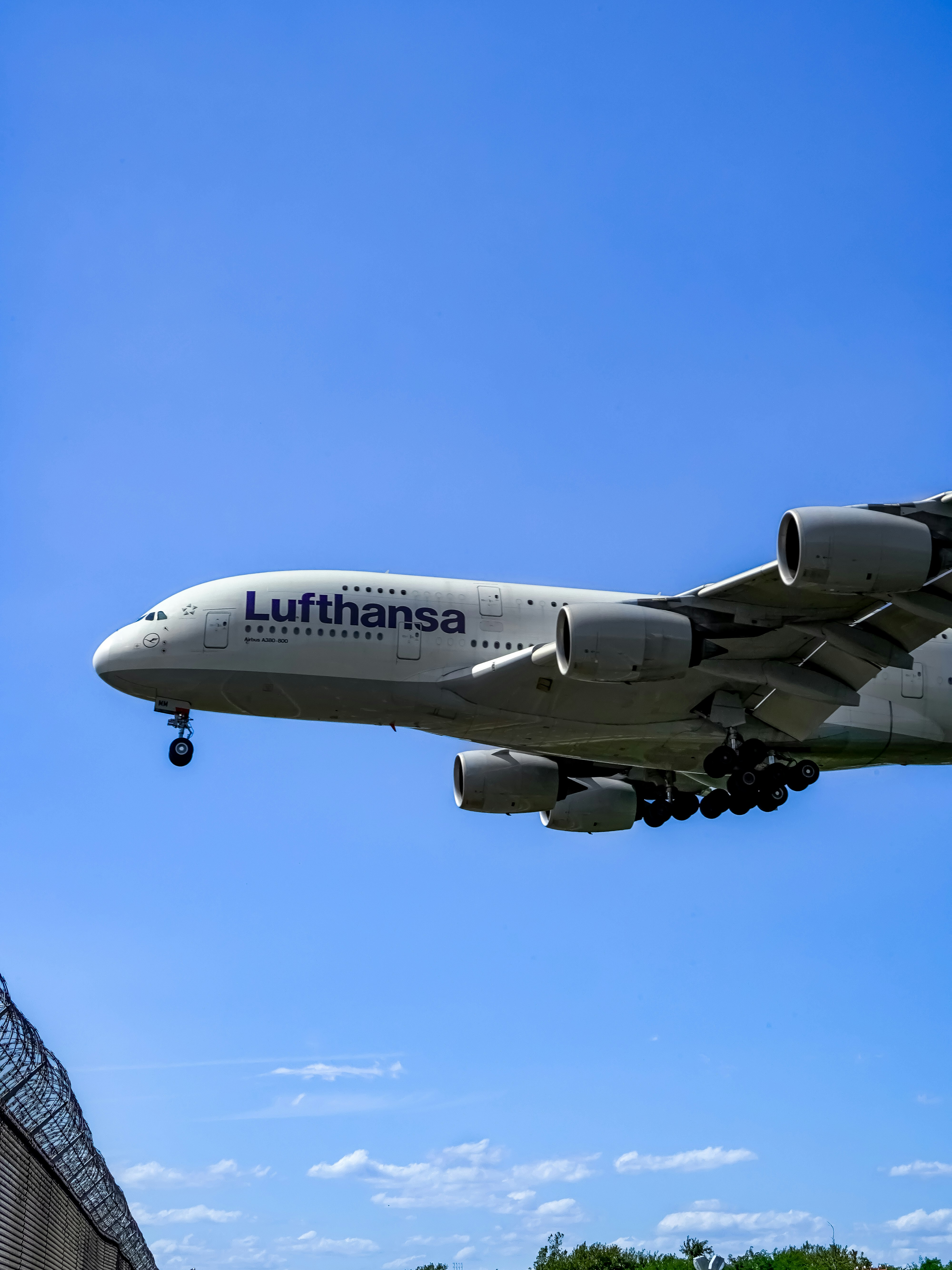 A Lufthansa Airbus A380 approaches for landing against a clear blue sky, showcasing its impressive wingspan and sleek design.