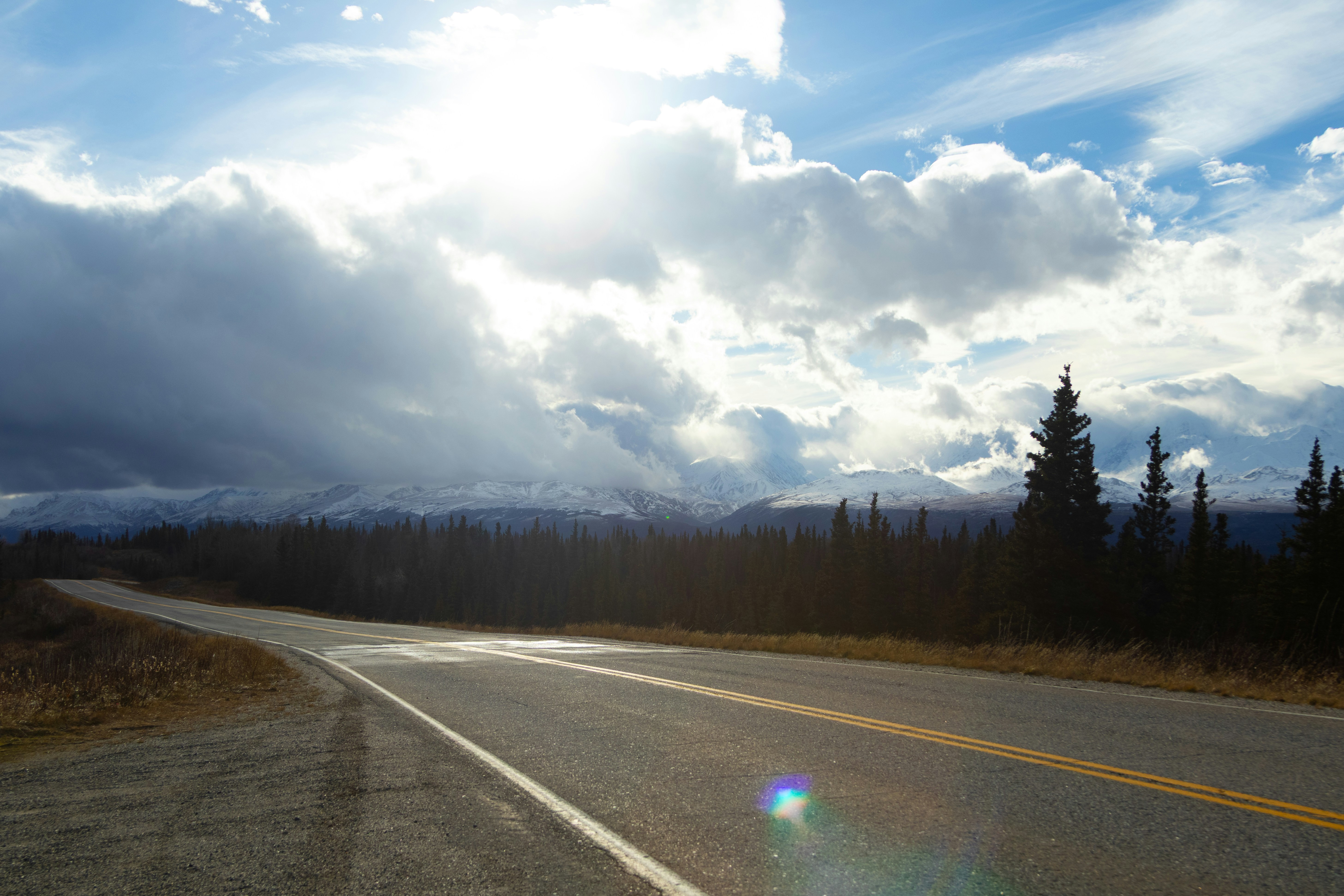 Curving road through a forested landscape under a dramatic sky, with sunlight breaking through clouds. The scene captures the essence of adventure and nature's beauty.