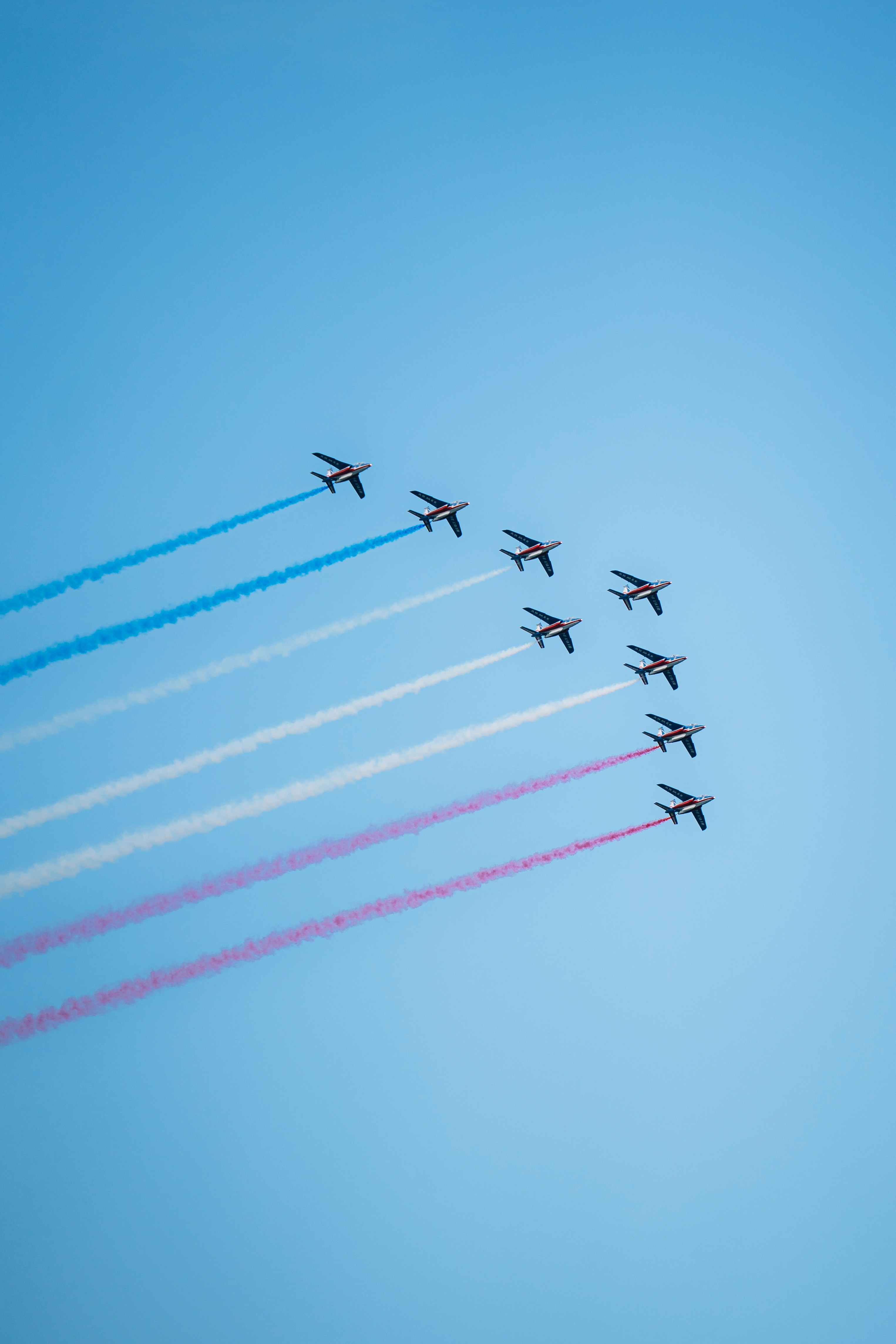 Nine planes fly in formation leaving colored smoke trails.