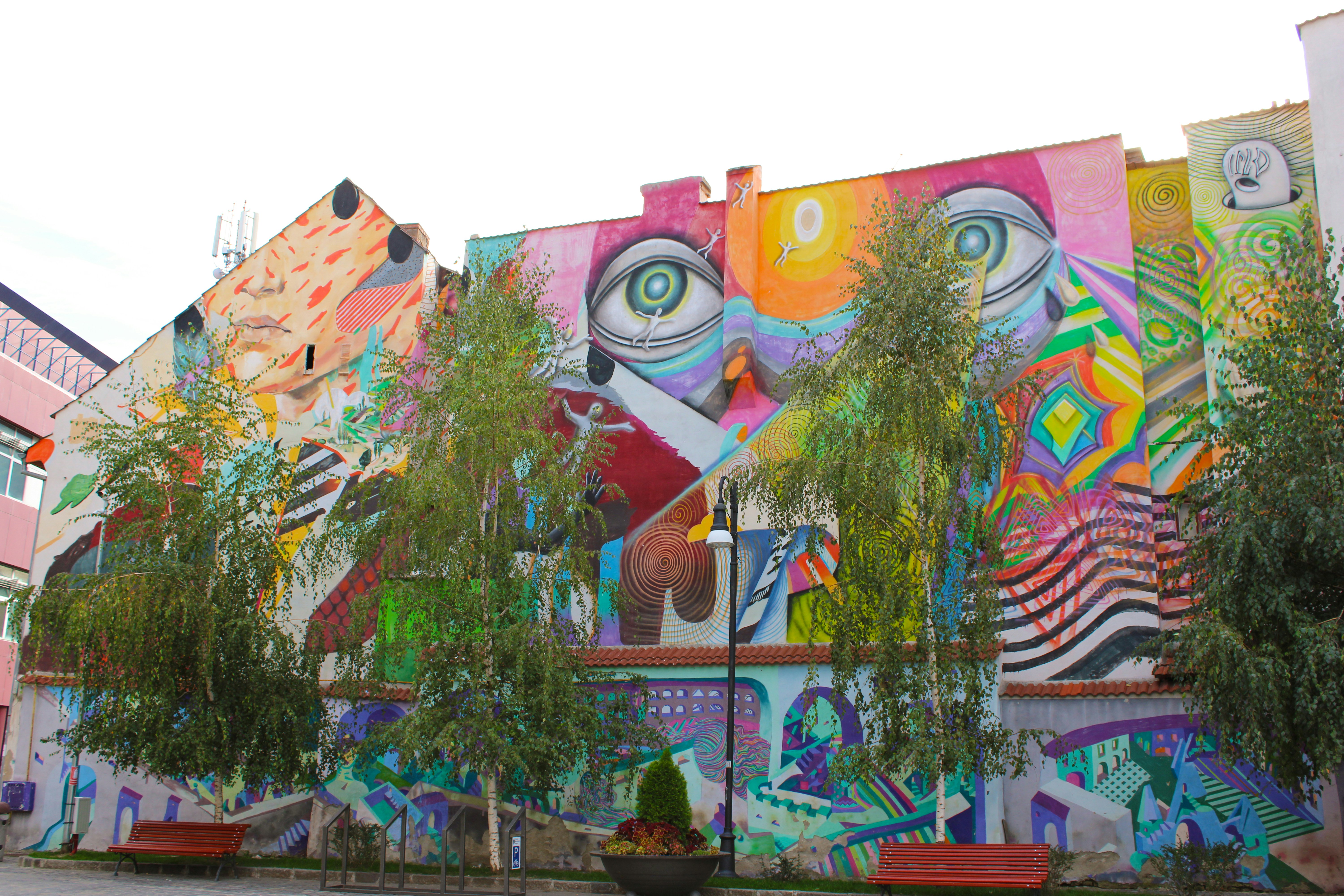 Colorful mural covers building with abstract art and eyes.
