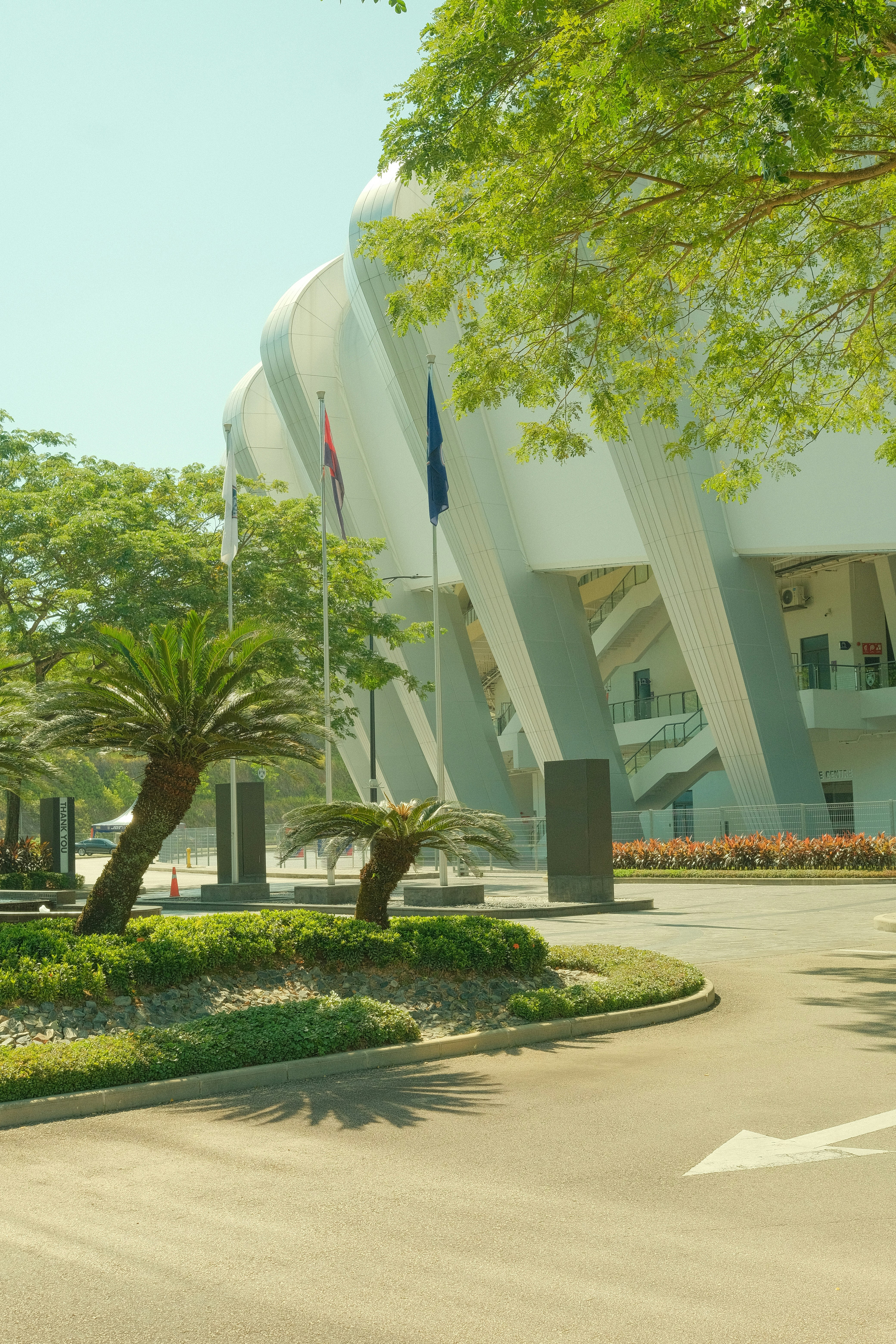 Modern stadium entrance with palm trees and greenery.