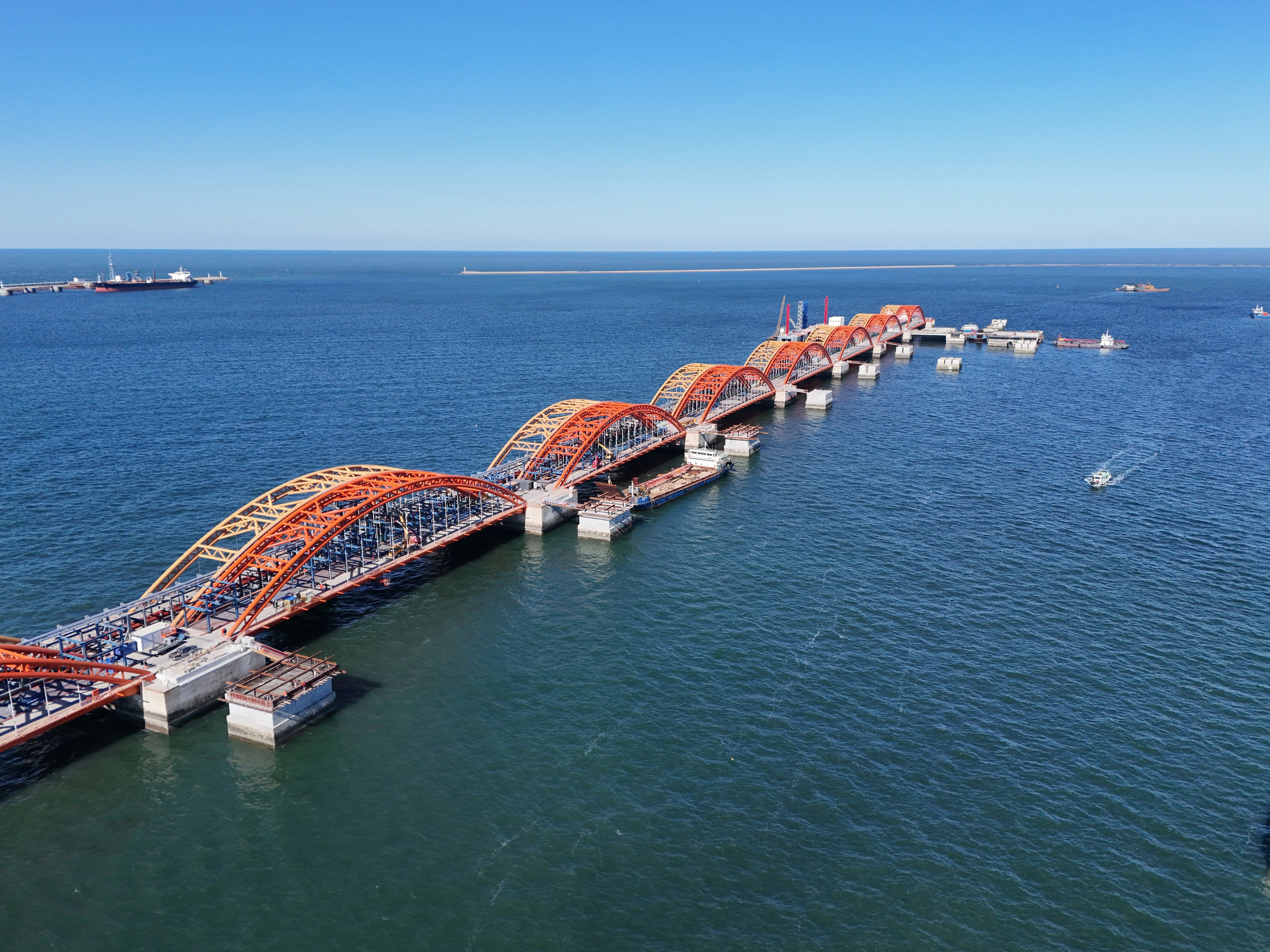Orange arched bridge over blue ocean water with ships.