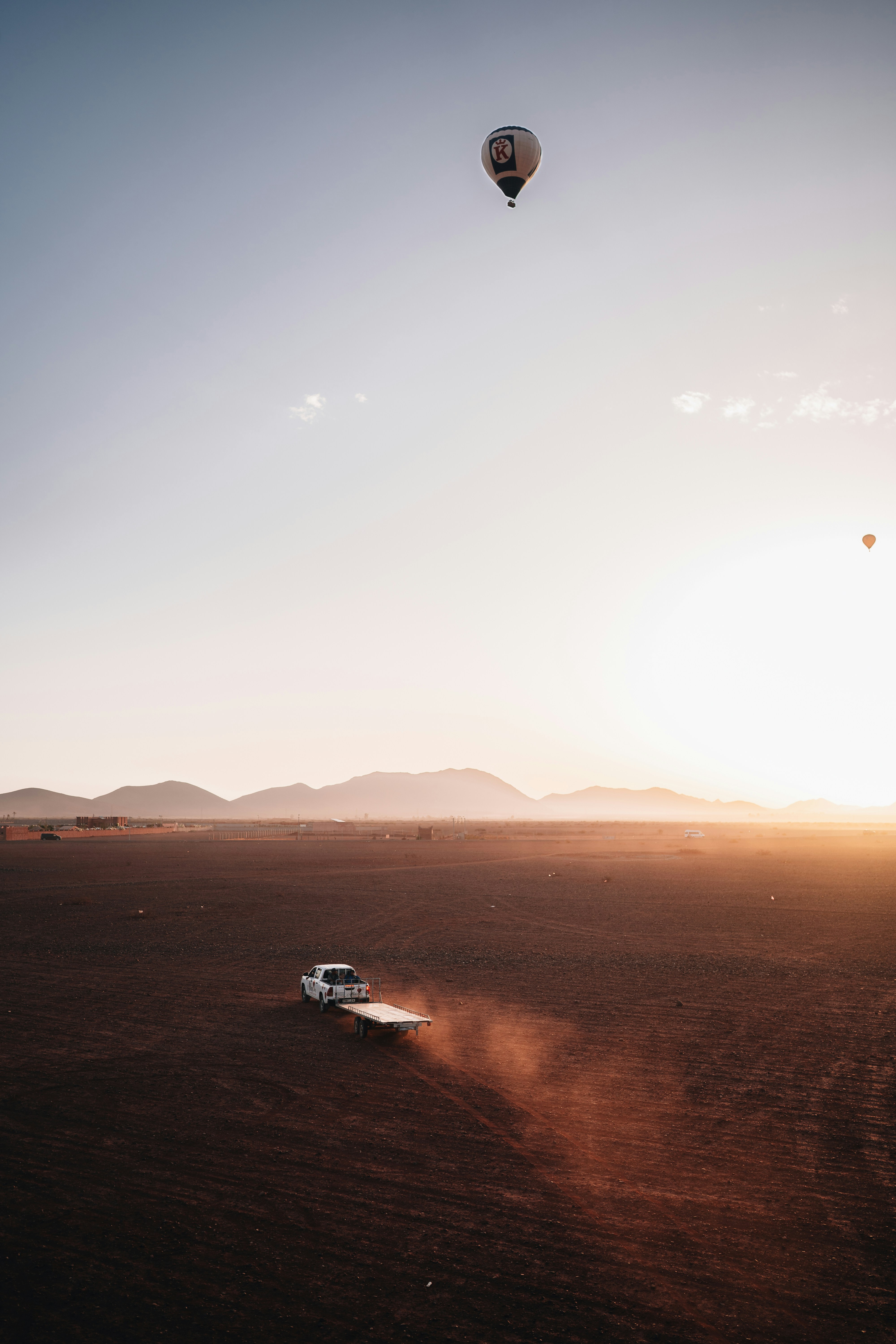 Hot air balloon flies over car in desert landscape