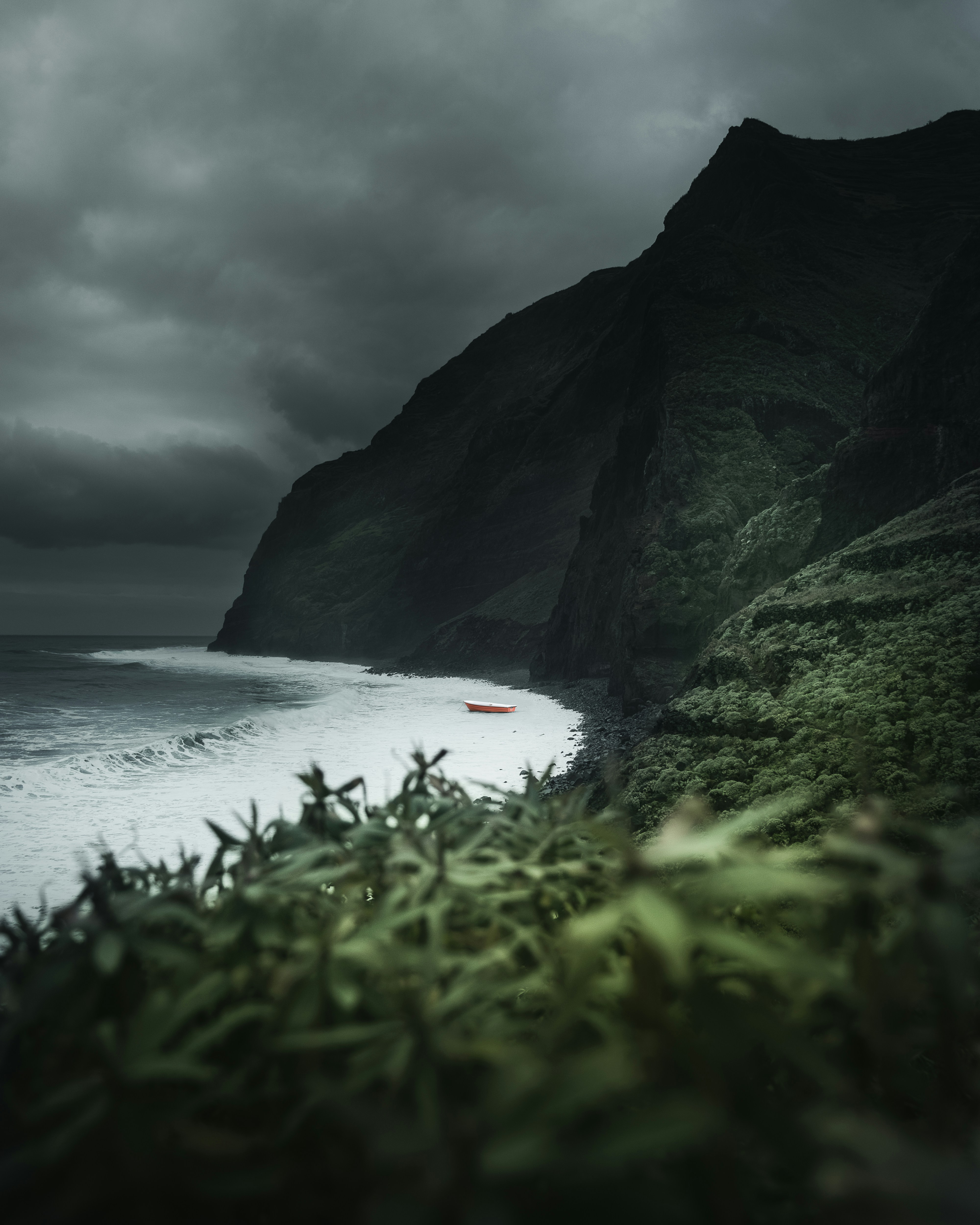 Red boat on a rocky shore with crashing waves.