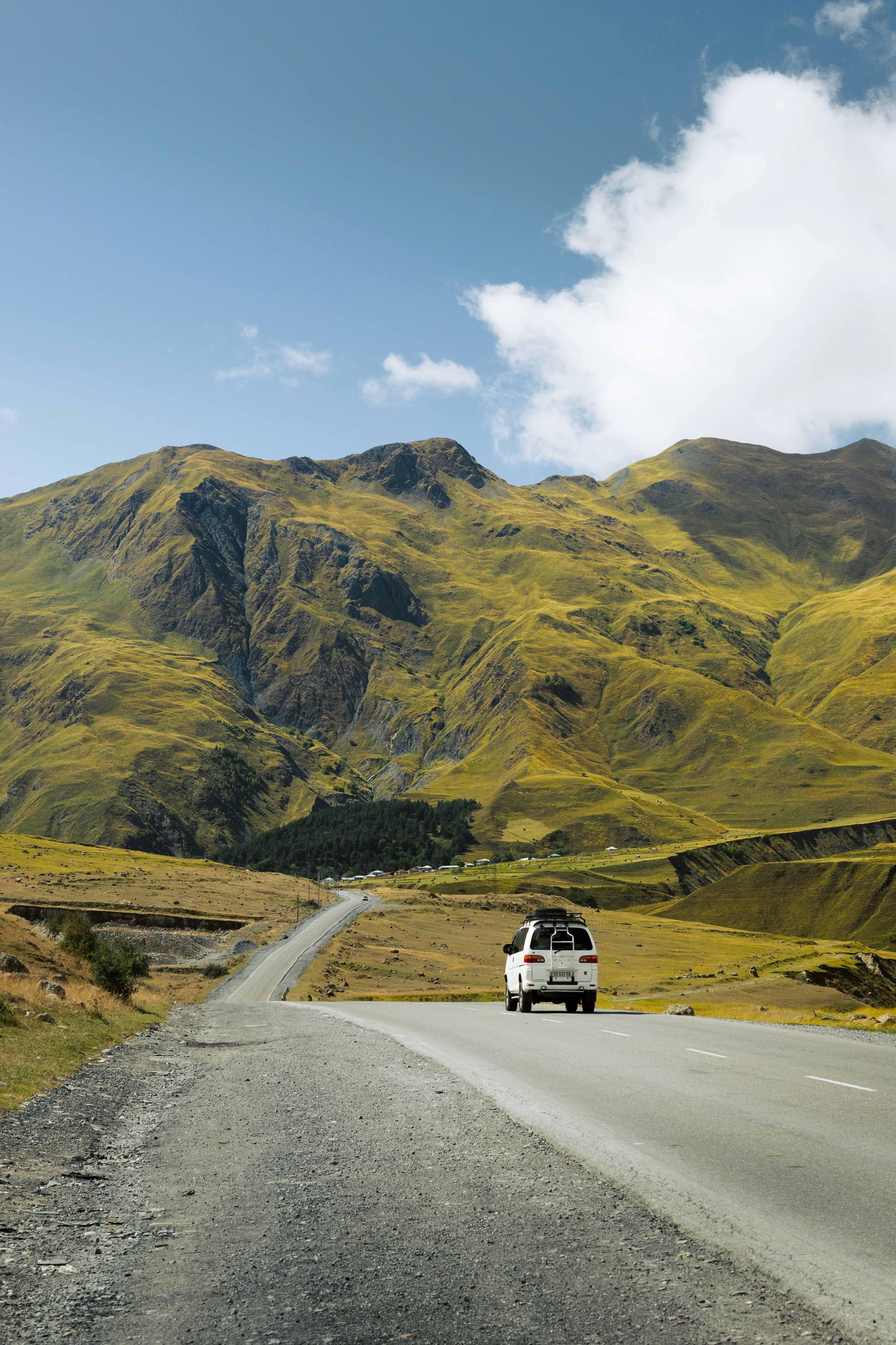 White car driving on a road towards mountains.