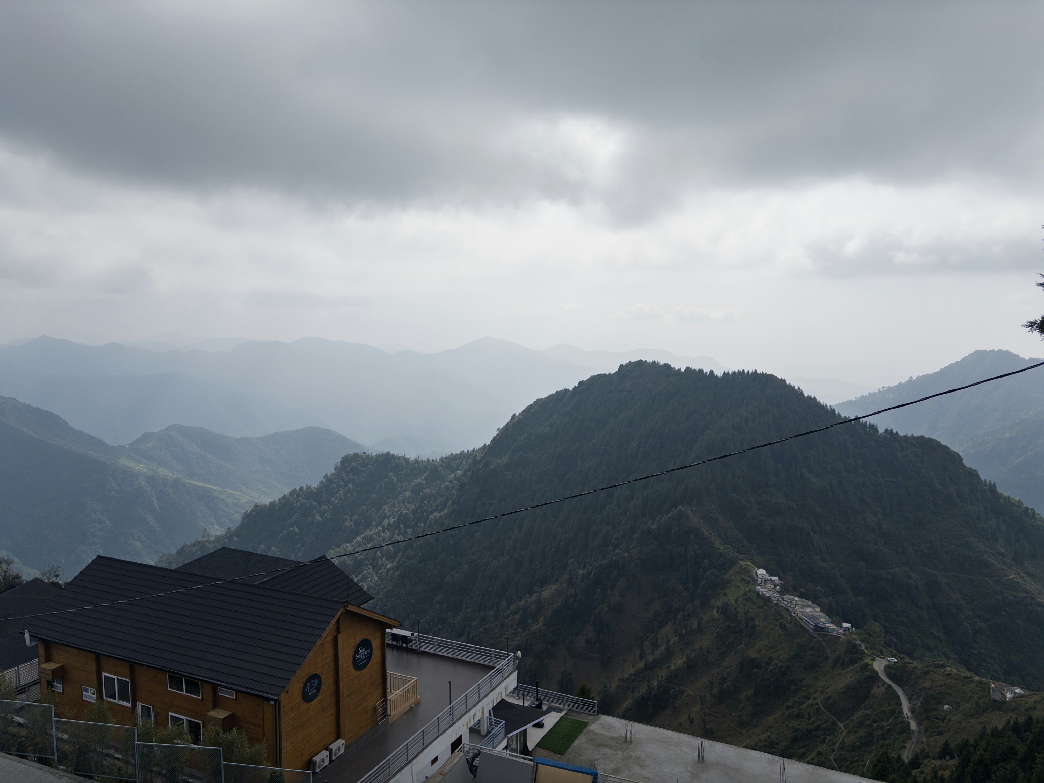 Lone wooden cabin perched on a mountainside, surrounded by rolling hills and a misty horizon.