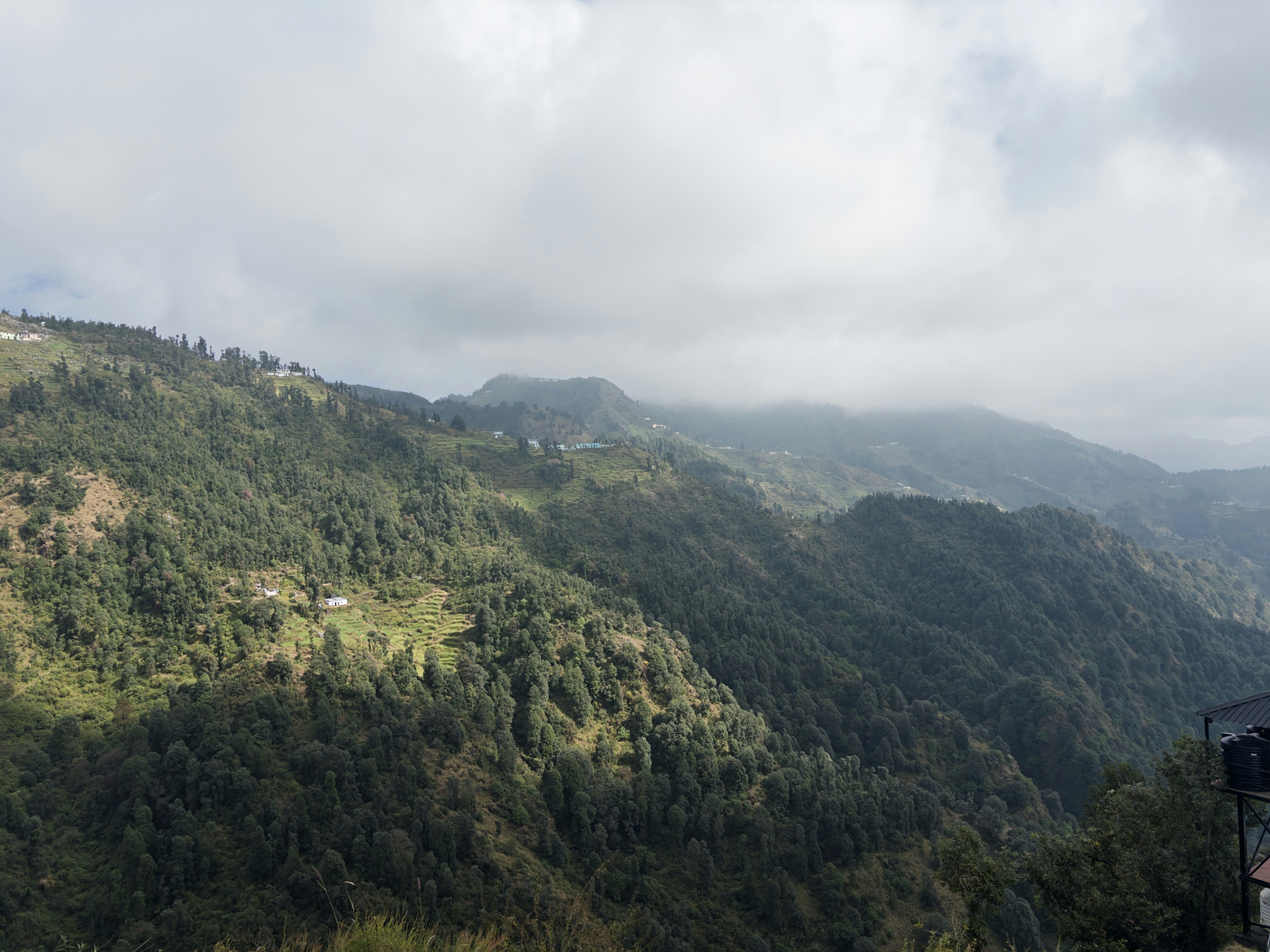 Lush green hillsides cascade down a mountain valley under a cloudy sky, showcasing the intricate patterns of nature's terrain.