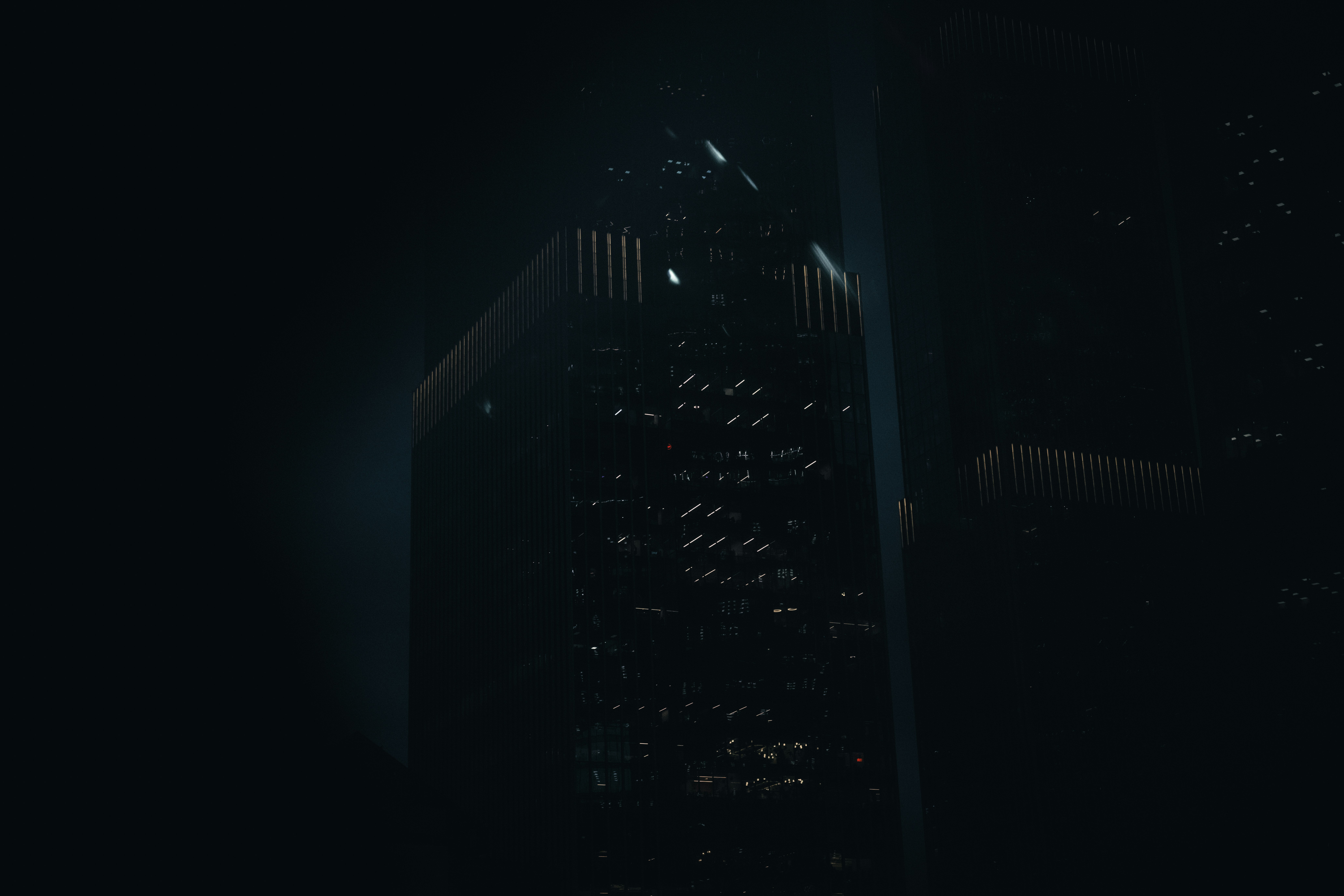 Dark skyscraper illuminated by city lights at night.