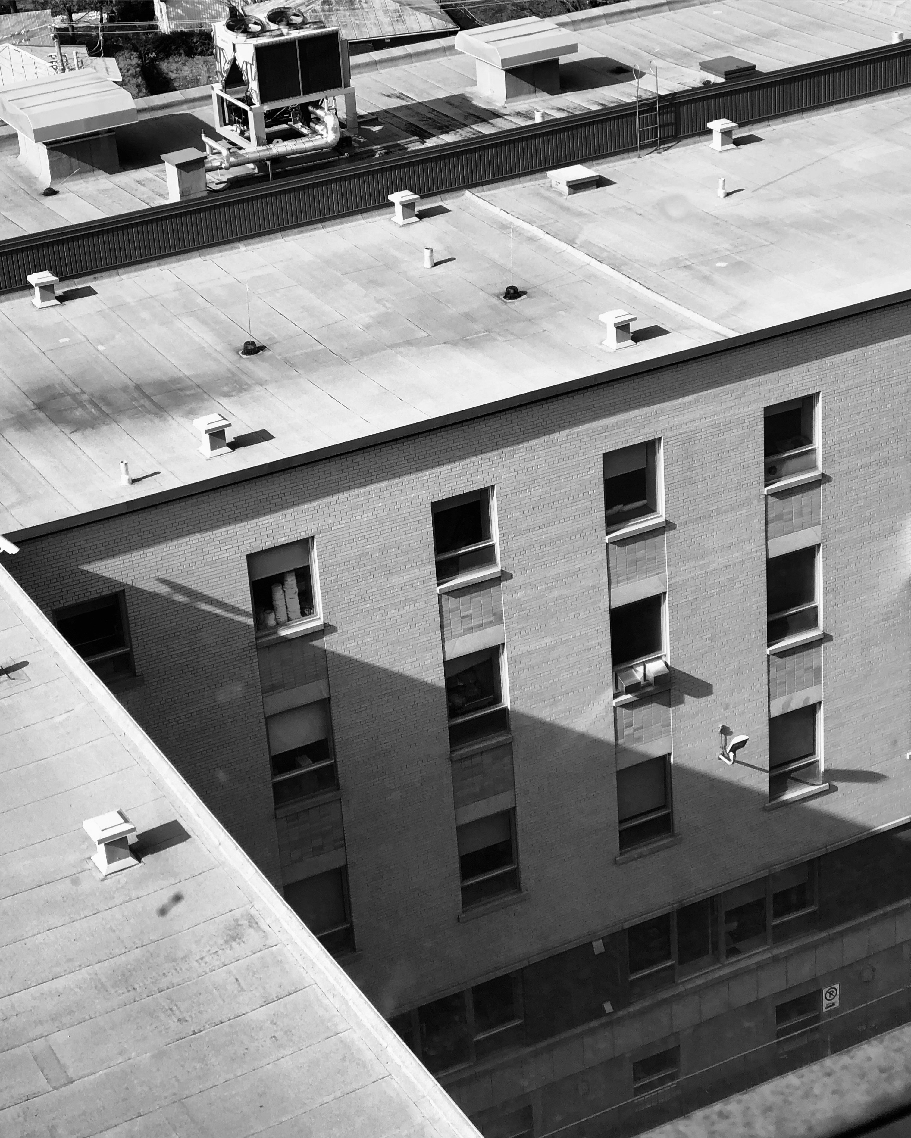 Black and white view of rooftops and building facades, showcasing the interplay of light and shadow in an urban environment.