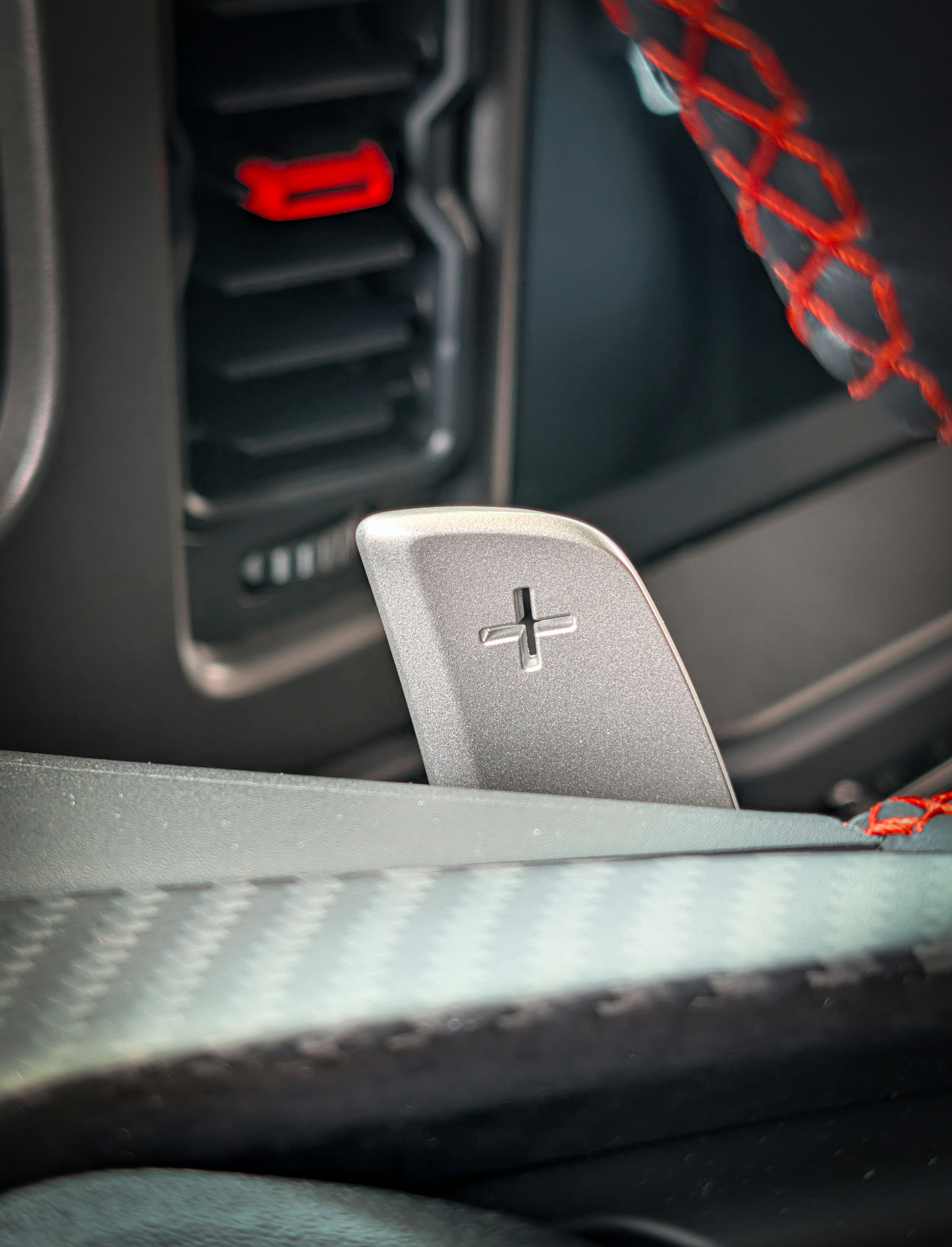This intense close-up embodies the raw, hands-on thrill of performance driving. The sharp focus on the metallic-finished paddle shifter, engraved with the essential 'plus' sign, instantly conveys speed and control. This high-tech element is framed dramatically by the sophisticated weave of the carbon fiber dashboard and the fiery contrast of the bold, hand-stitched red thread, creating an exquisite fusion of race-inspired mechanics and bespoke luxury. Boulevard Ford in Millsboro