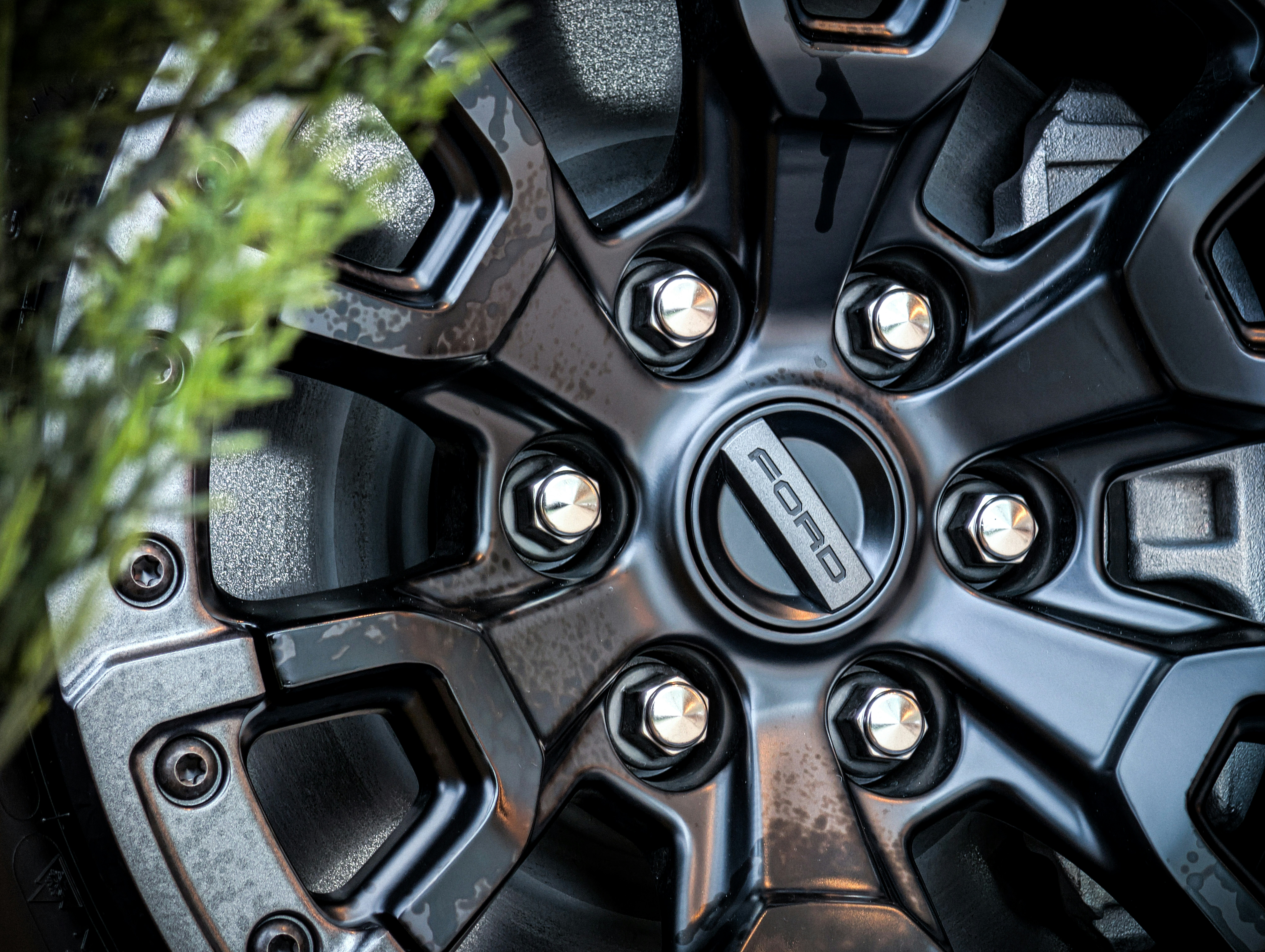 Close-up of a Ford wheel showcasing intricate design and craftsmanship, framed by foliage.
