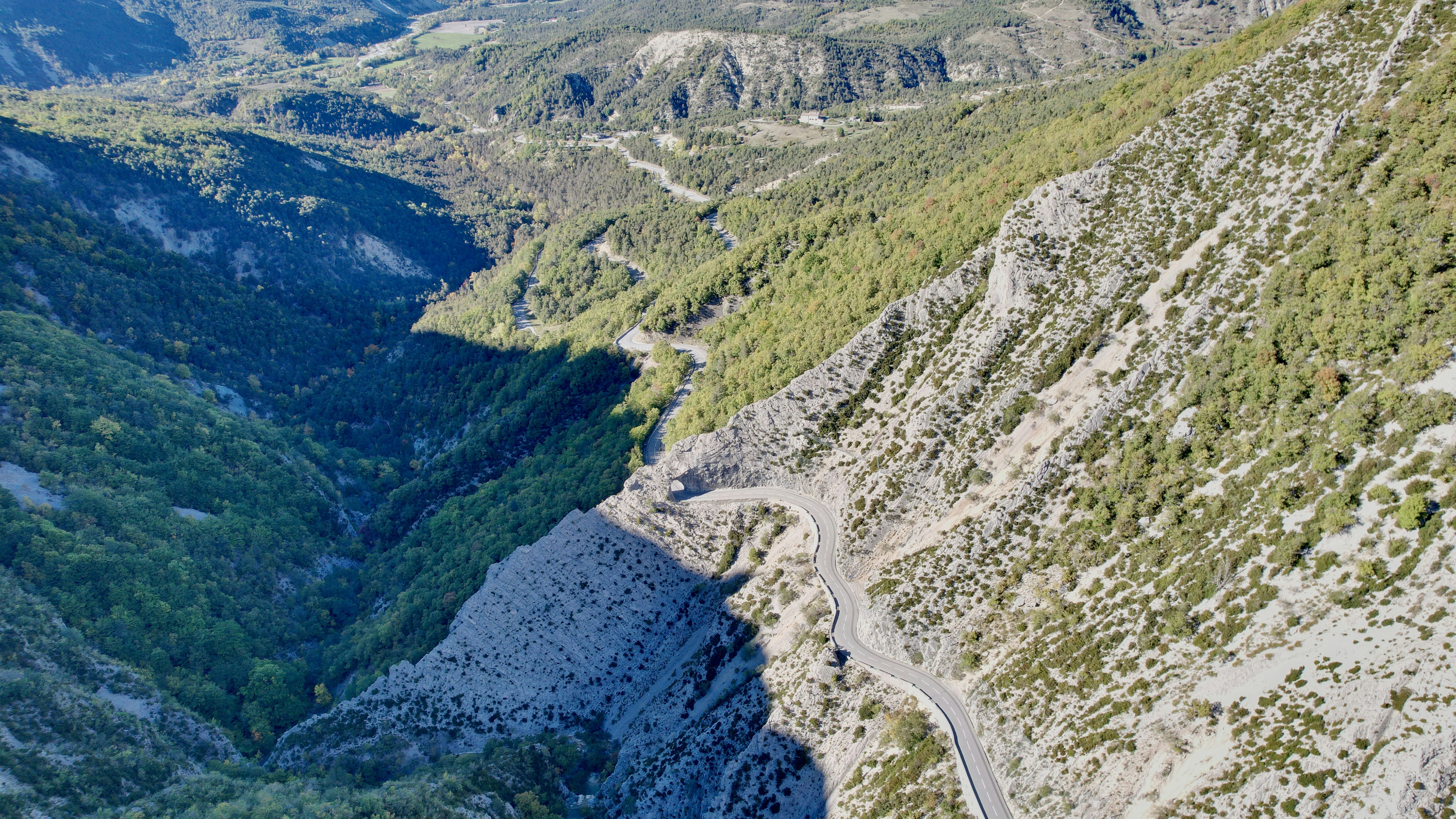 Aerial view showcasing a winding road carved through a lush valley surrounded by rugged cliffs and dense foliage.
