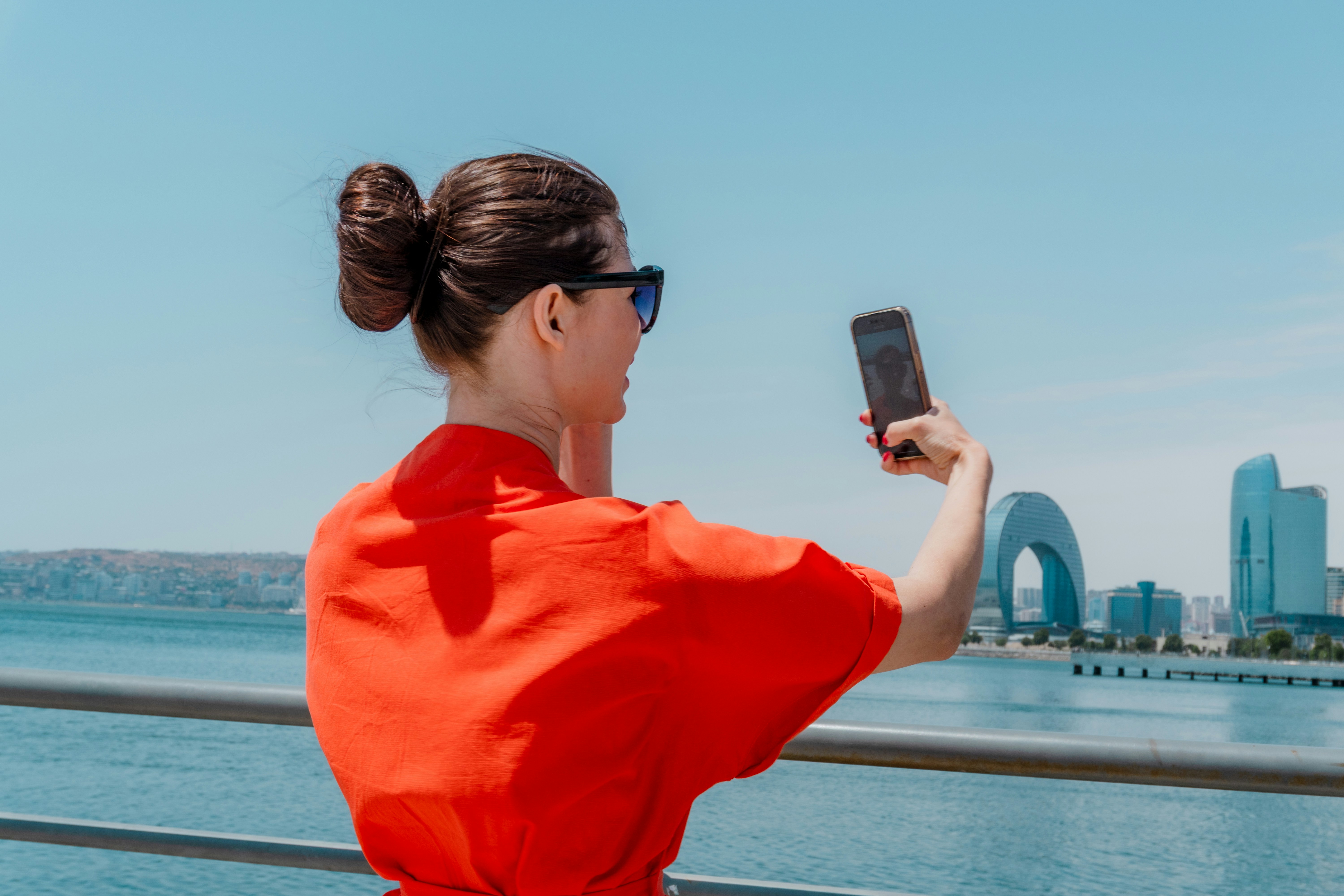 Harbor Selfie in Orange Light: A Back-Turn Moment Against a Modern Waterfront Skyline