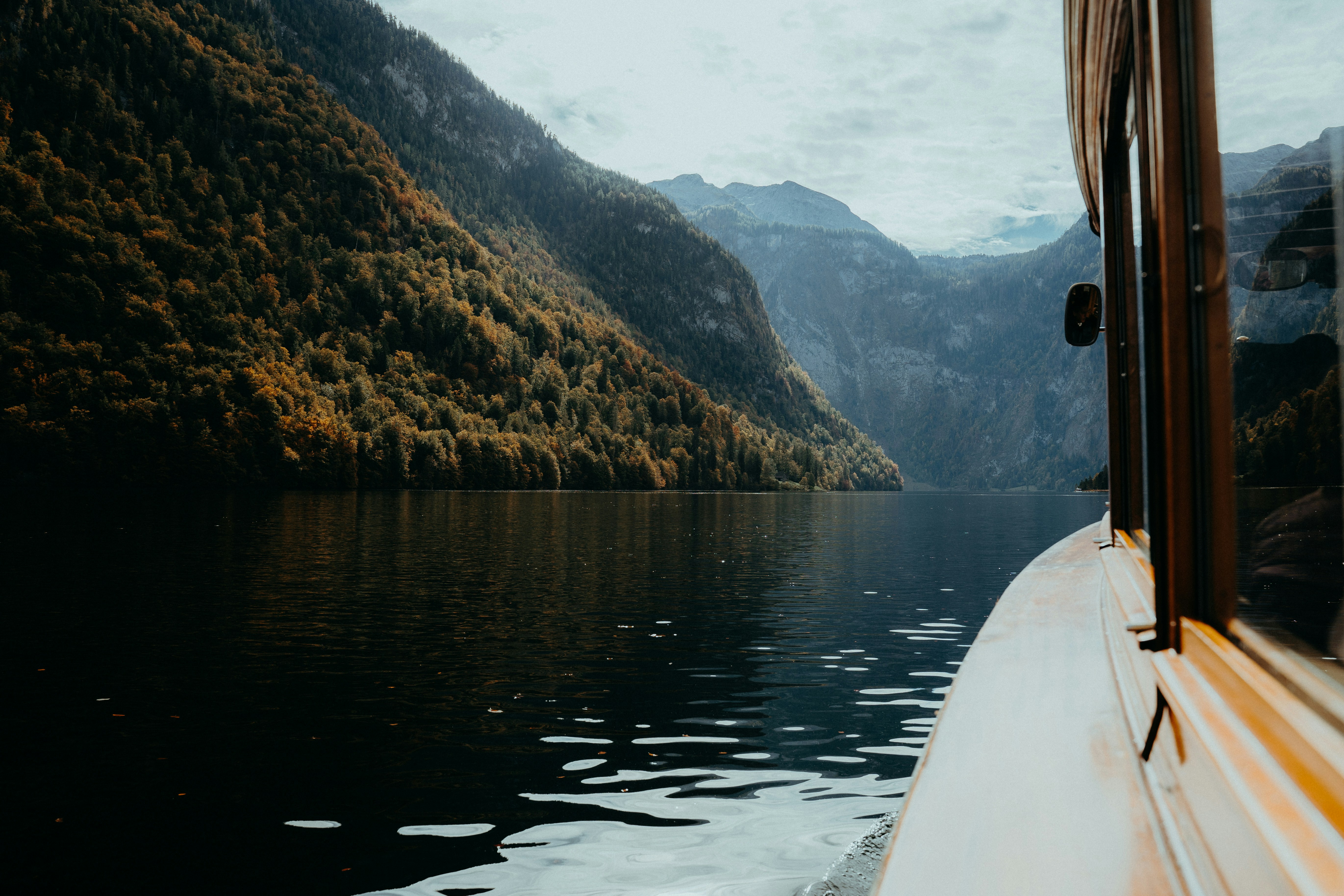 Königsee Berchtsgardn | Boat traveling on a calm lake with mountains.