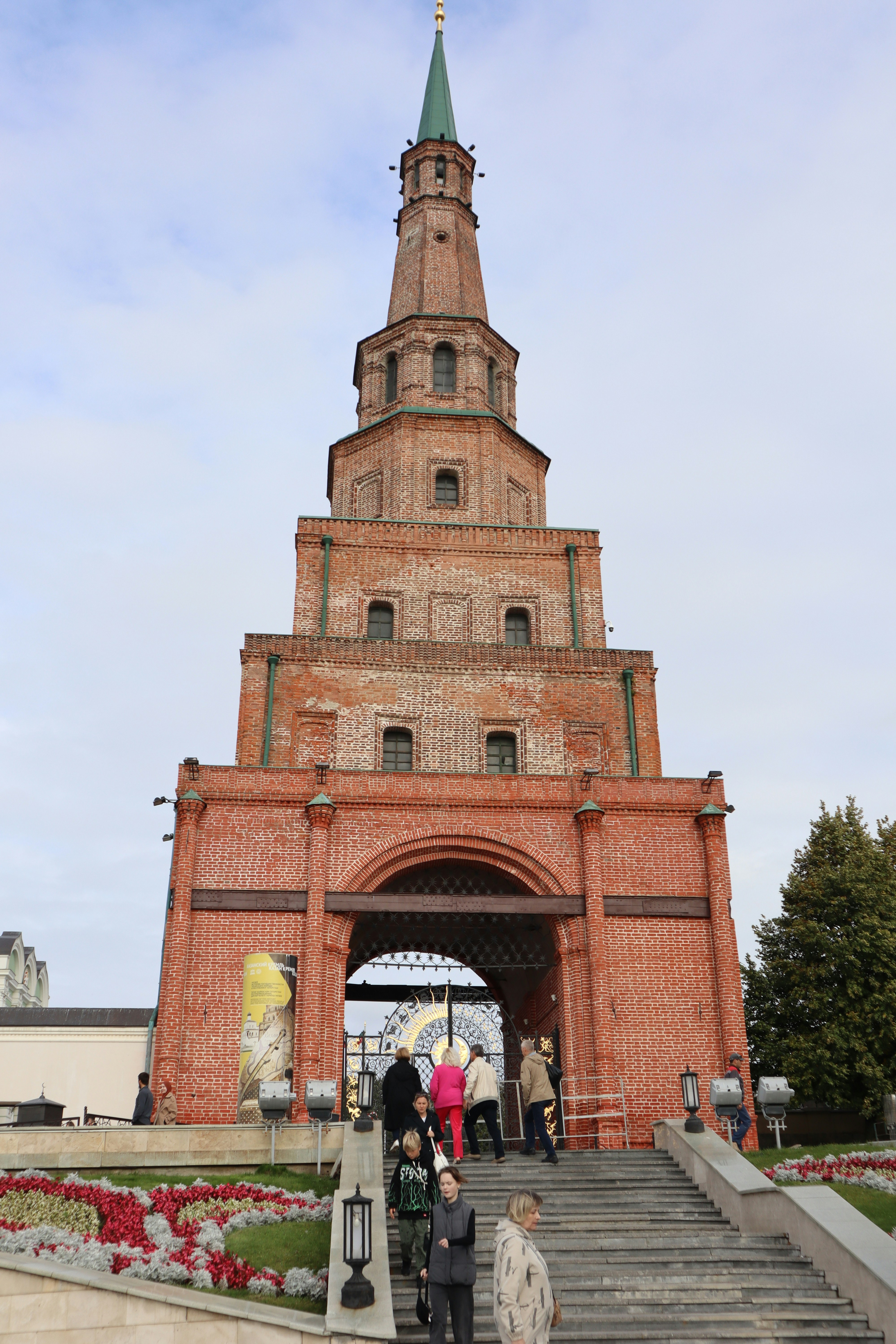 People ascend stairs to a brick tower with a spire.