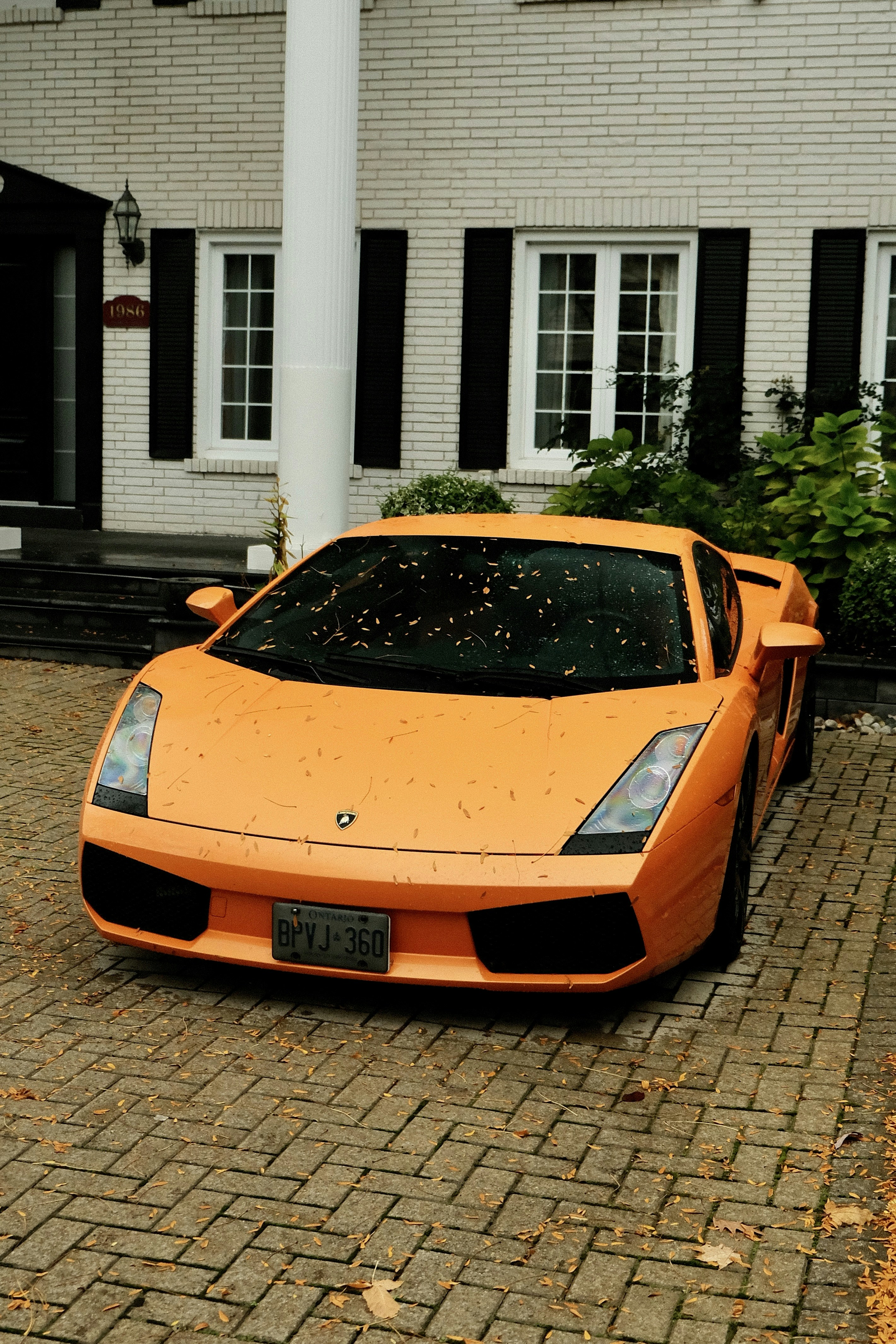 Orange Lamborghini on Brick Driveway Beneath Classic White Facade