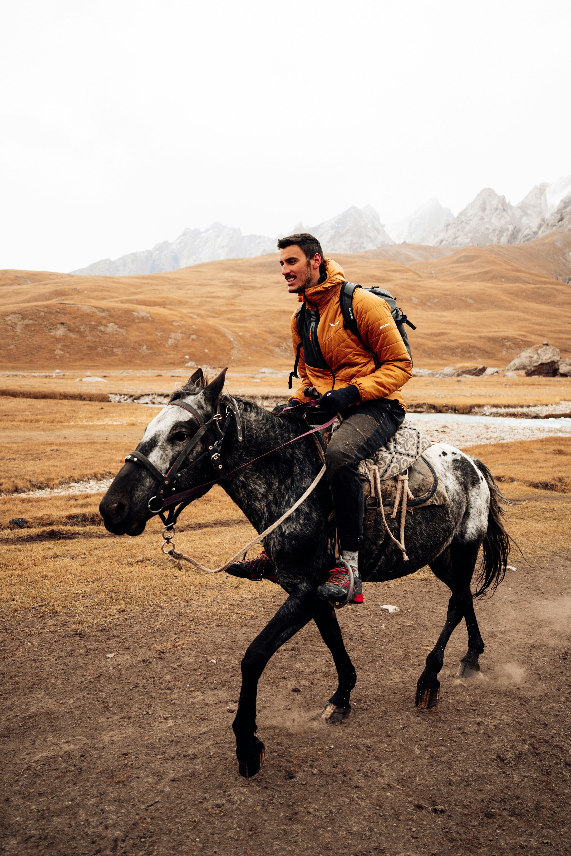 Man rides a speckled horse through a dry landscape.