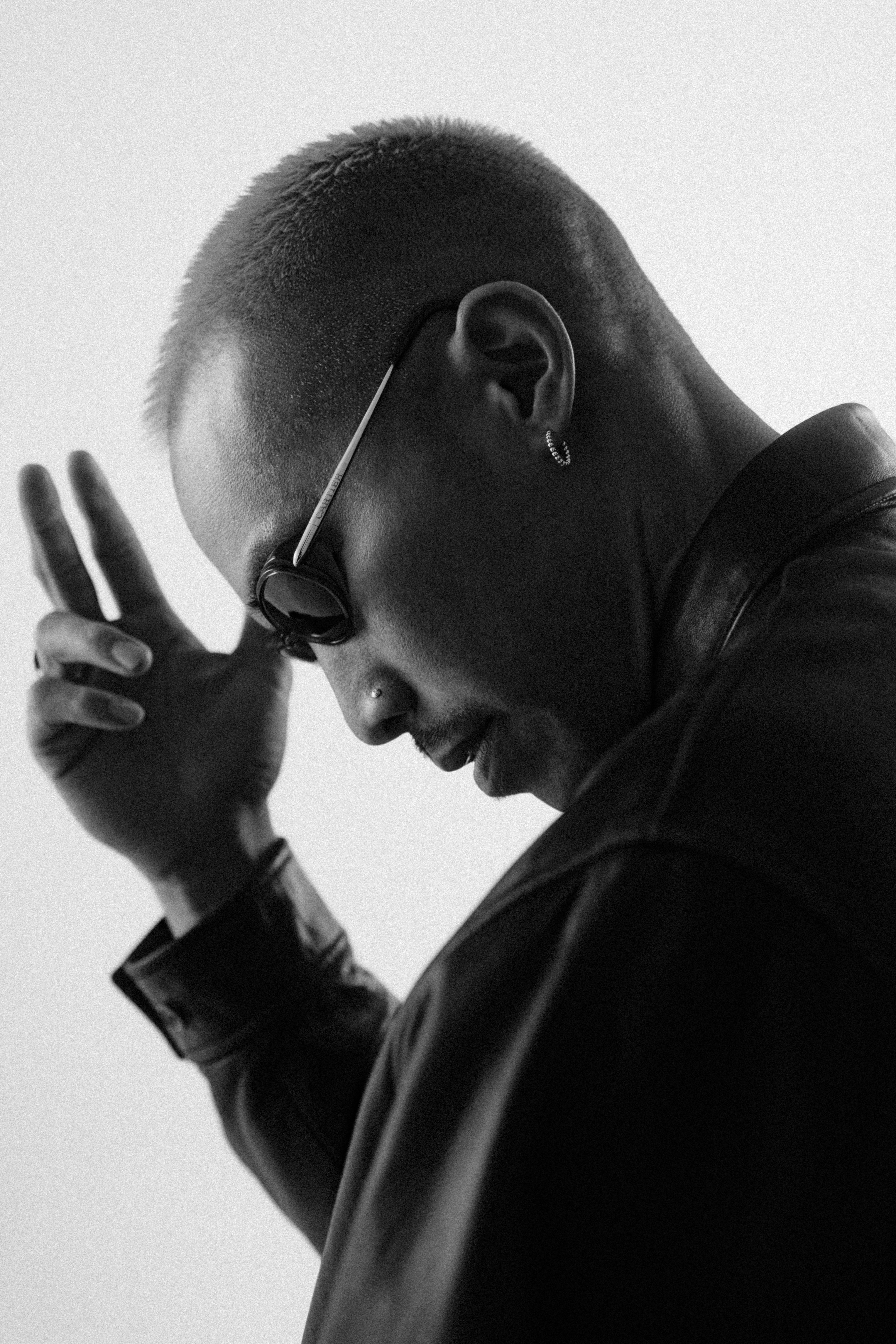 A monochrome portrait of a man in sunglasses, exuding an air of contemplation and style. His hand gestures suggest a moment of reflection.